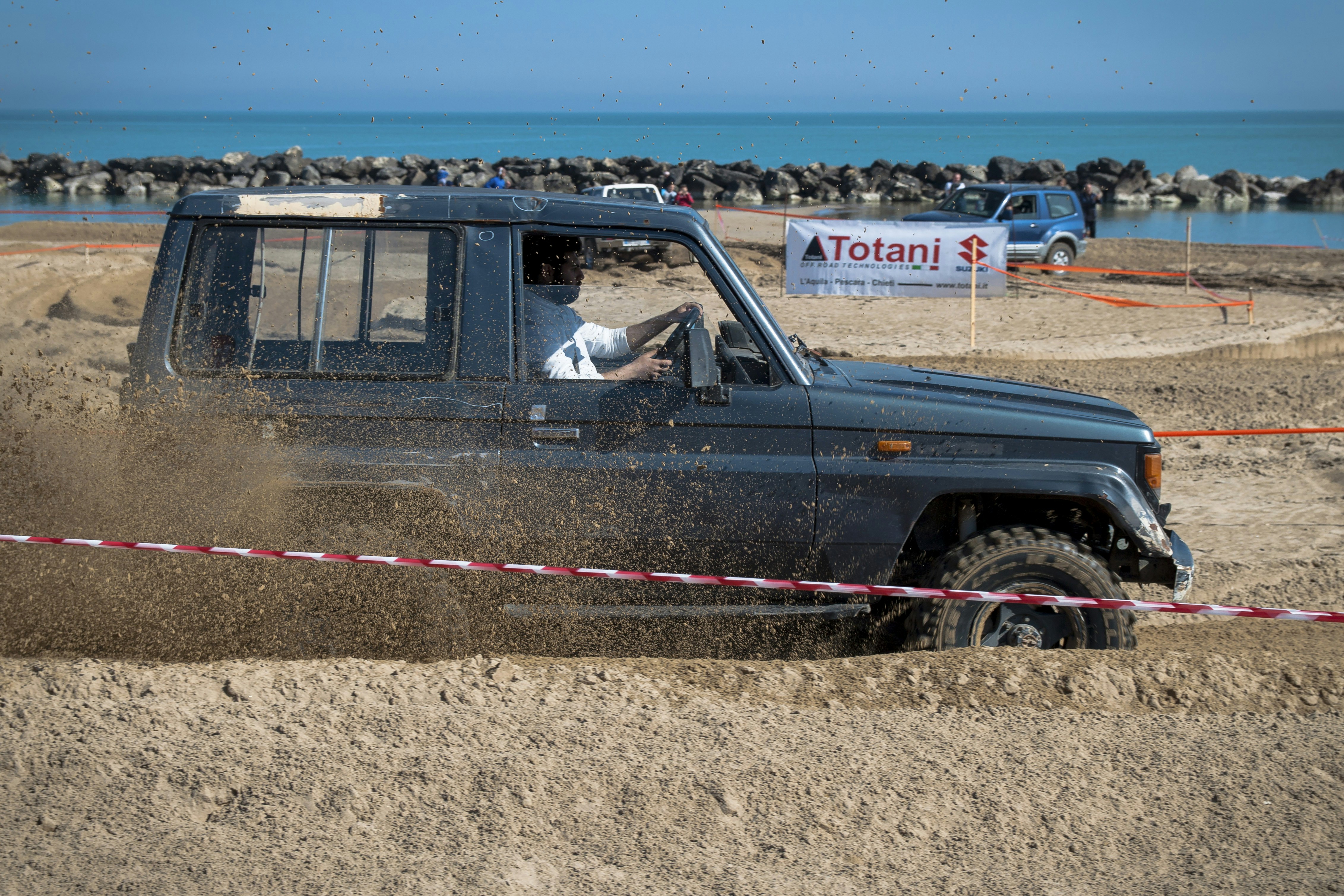 Off-road vehicle navigating a sandy beach track with the ocean in the background.