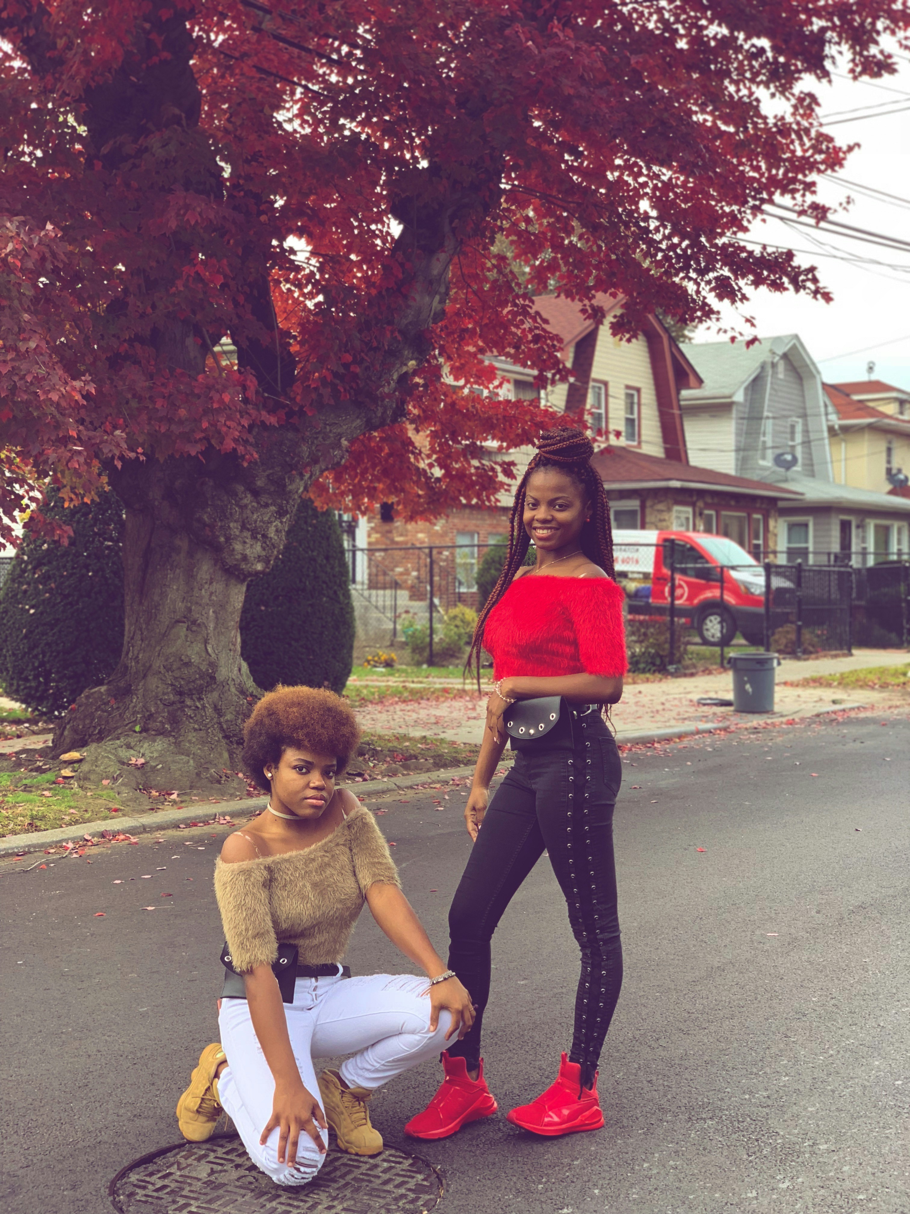 Two fashionable individuals pose confidently on a suburban street, framed by vibrant autumn foliage. The scene captures a blend of style and seasonal beauty.