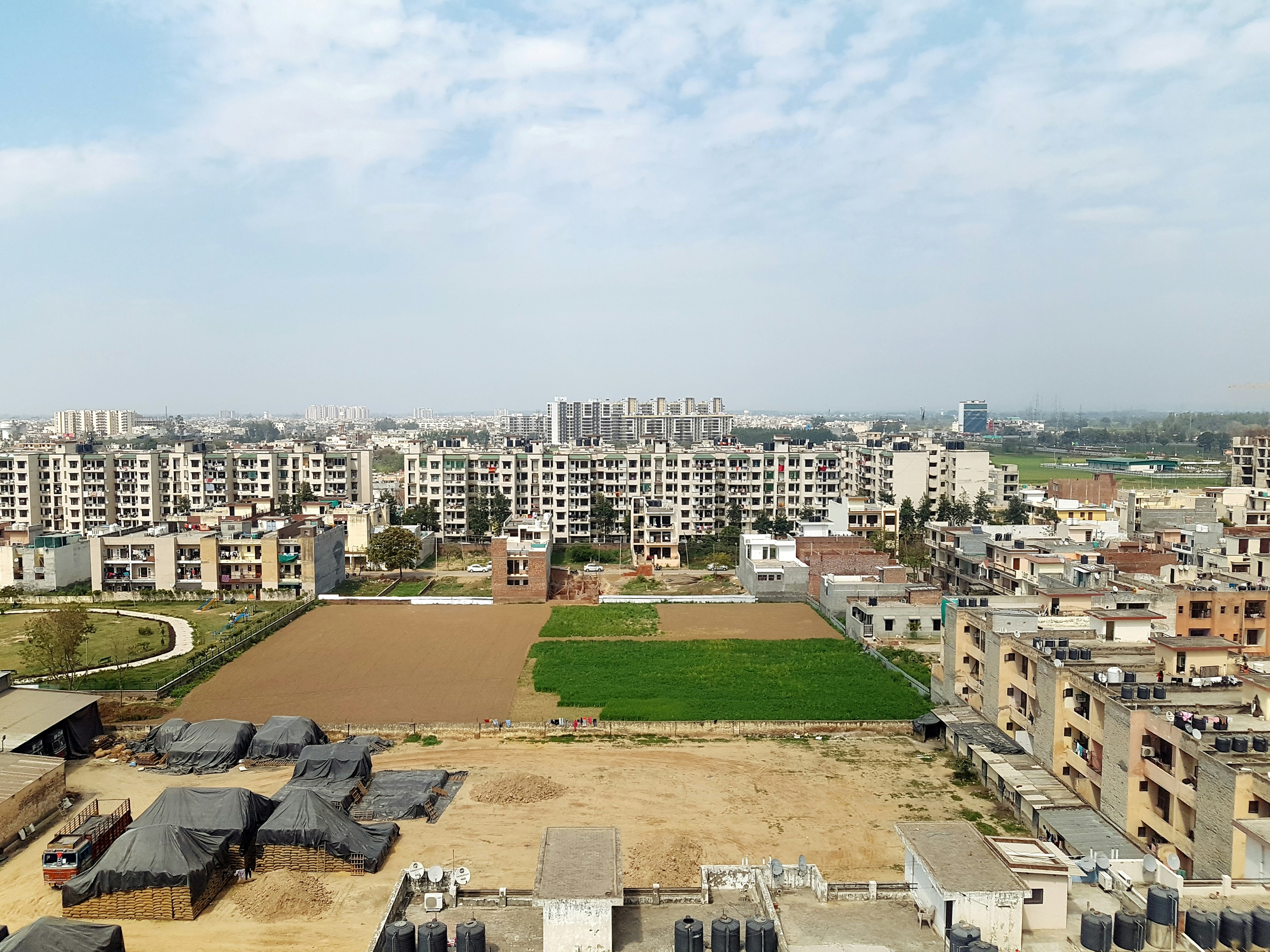 Cityscape with construction sites and green fields under a partly cloudy sky.