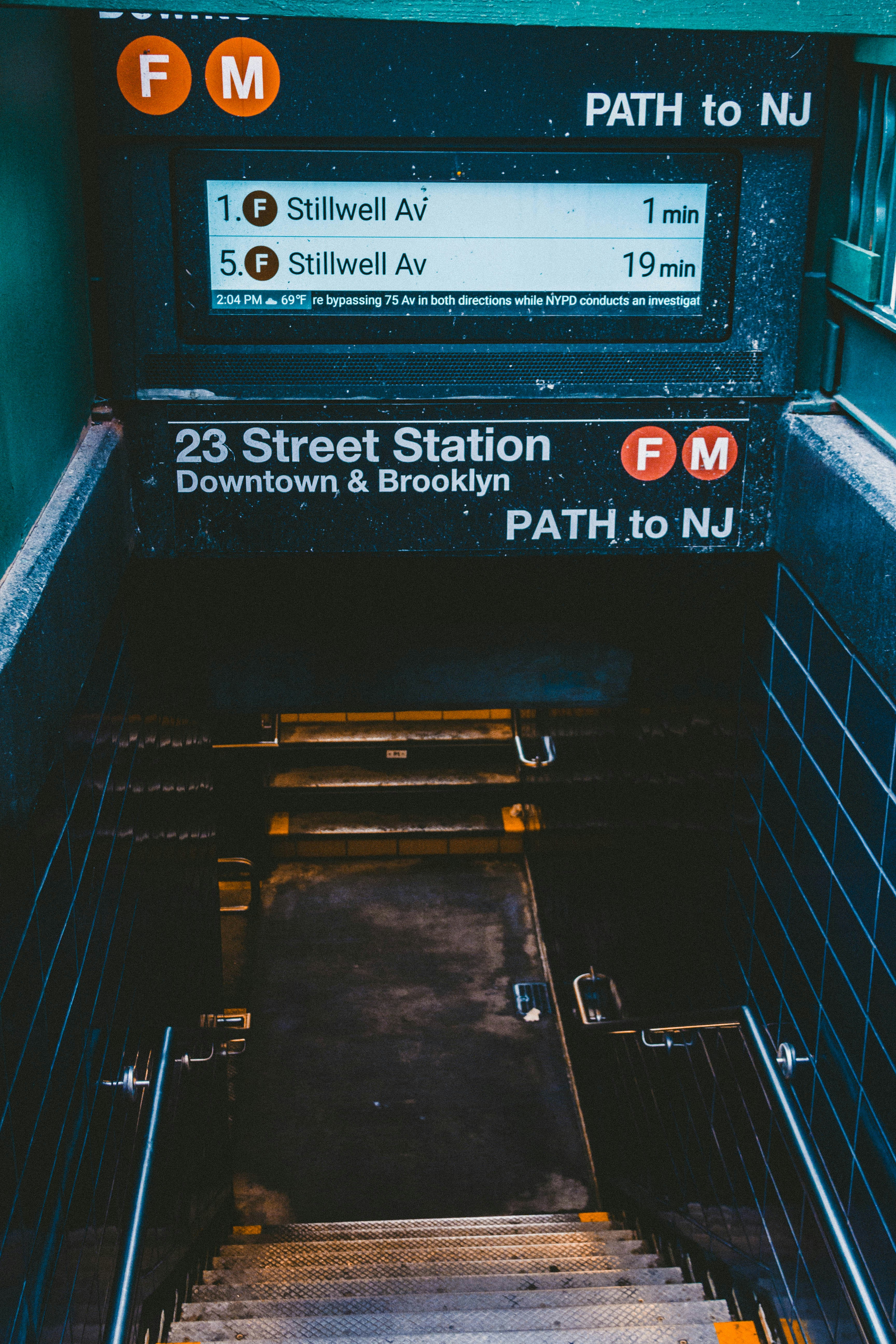 Subway station signage directing commuters towards the PATH to New Jersey, featuring arrival times for trains. The setting captures the essence of urban transit life.