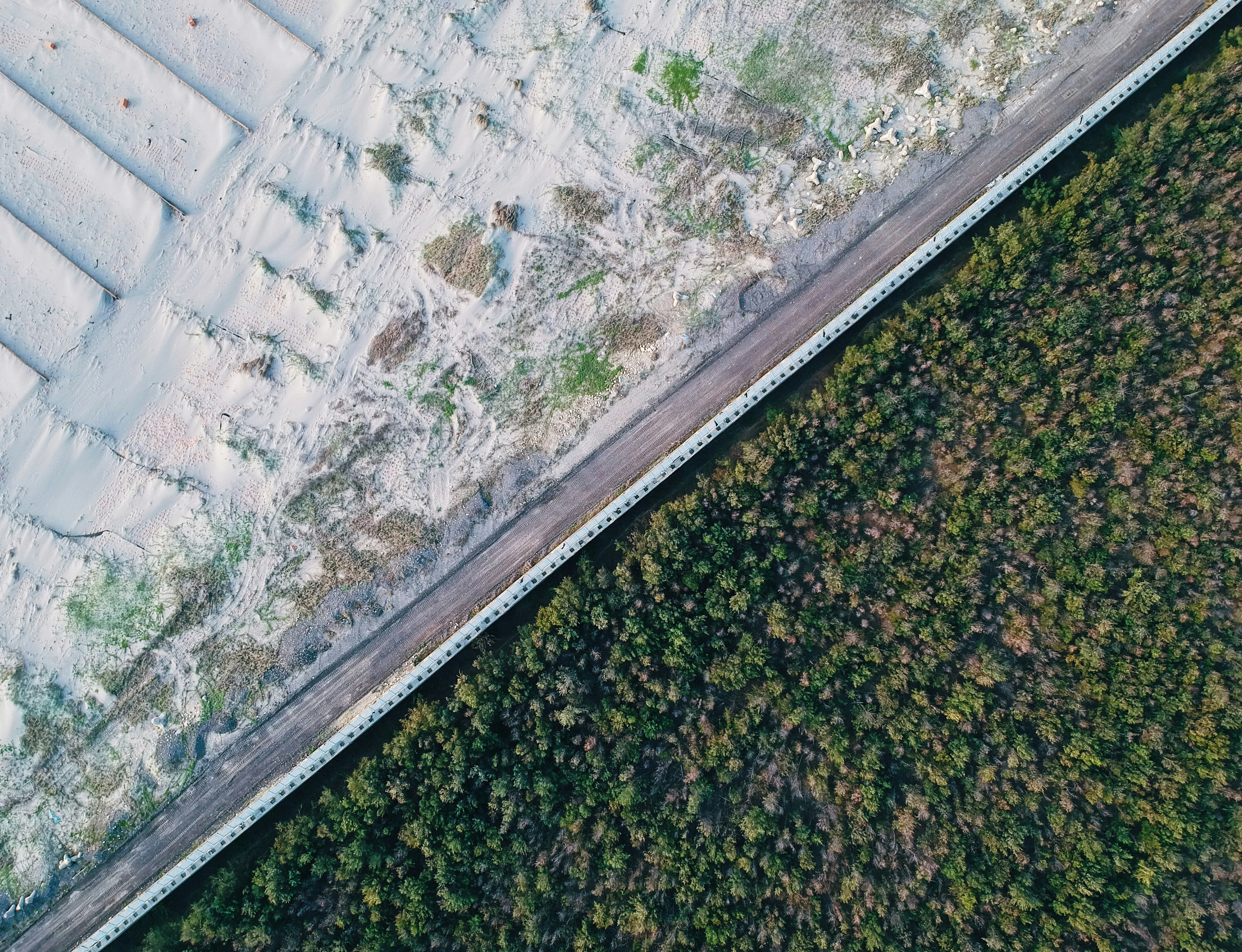 Aerial view showcasing the stark contrast between a sandy industrial landscape and a dense forest, highlighting the boundary between nature and human activity.