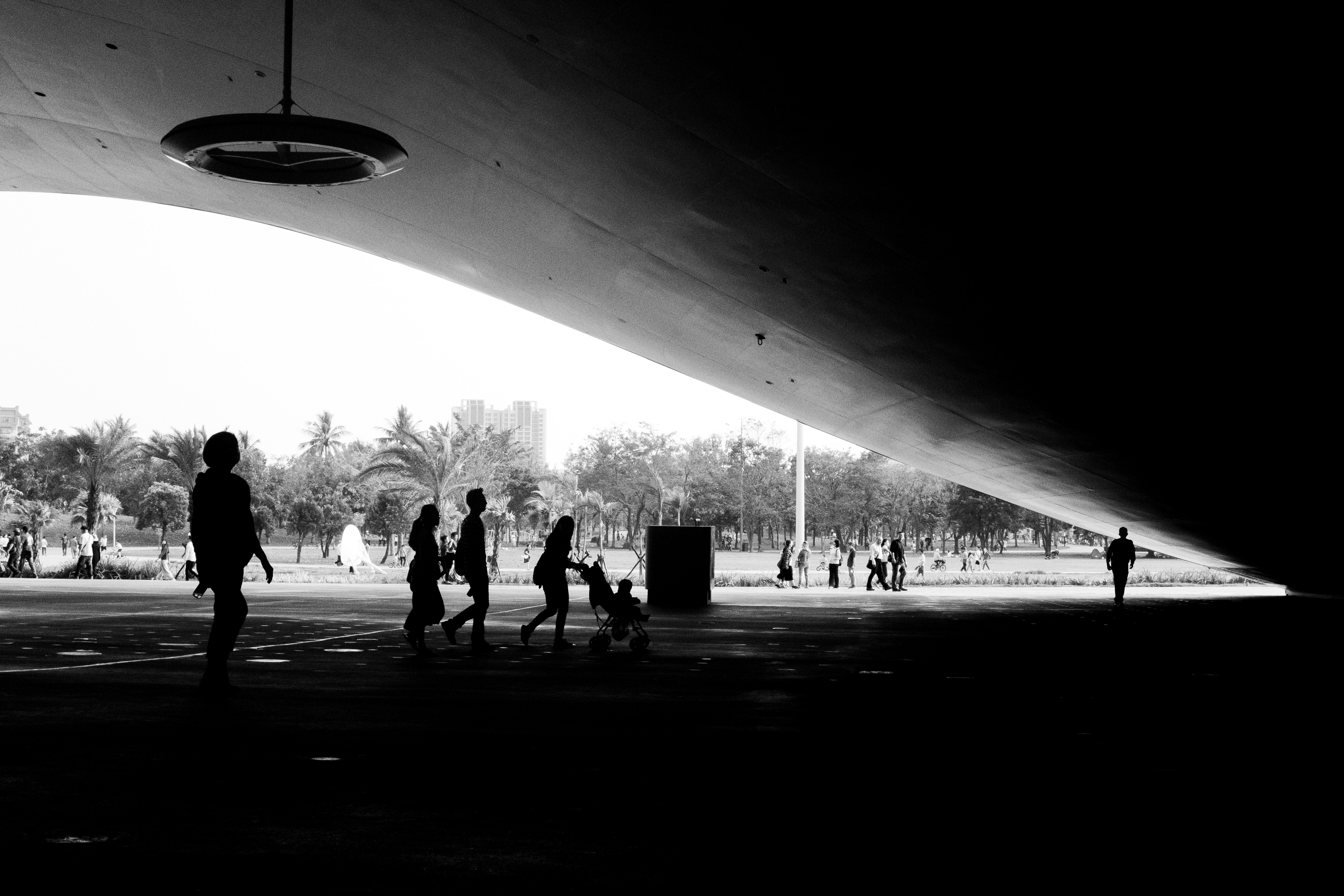 Silhouetted figures under a vast concrete canopy with a cityscape in the background.