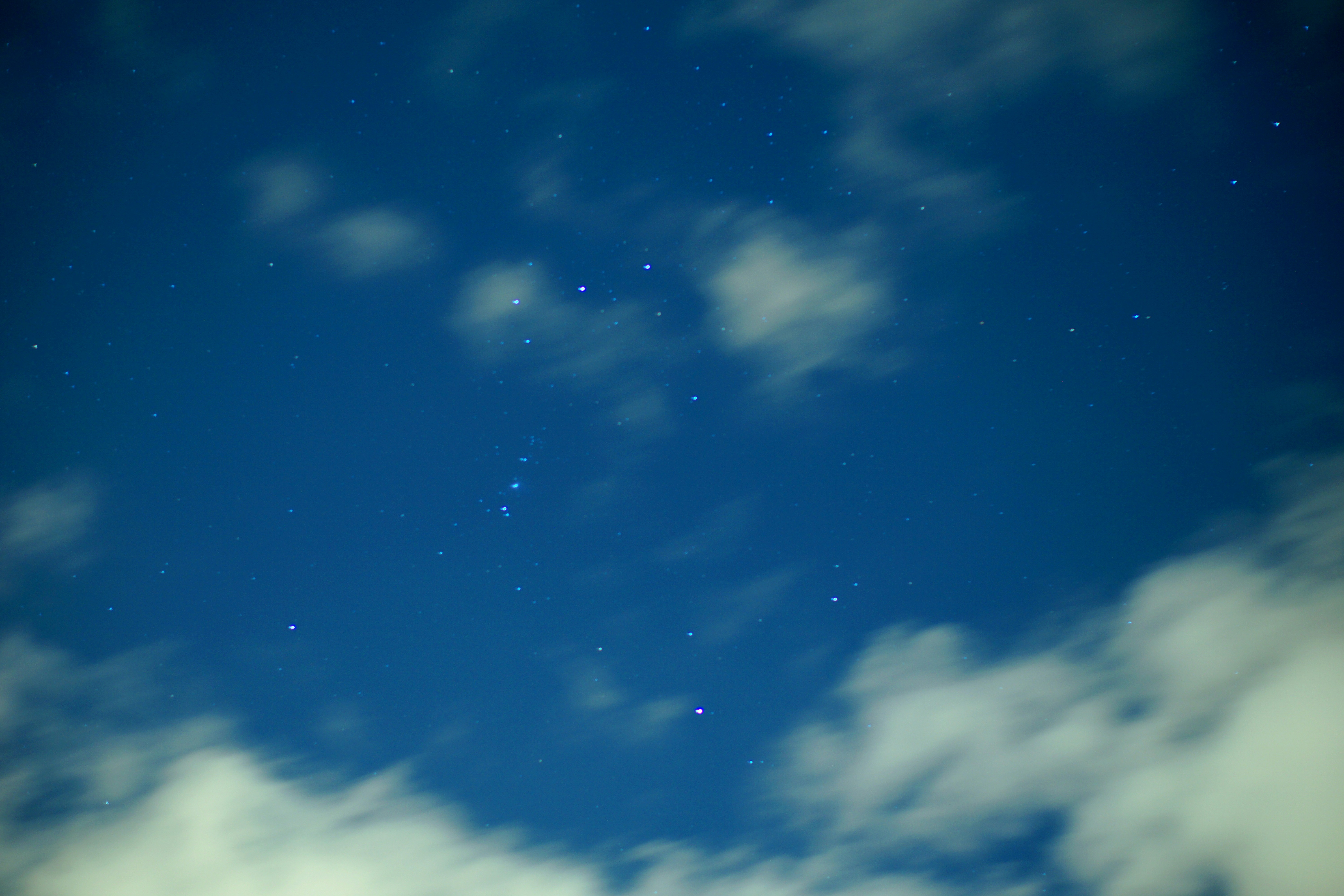 Stars twinkle through a scattering of blurred clouds in a night sky.