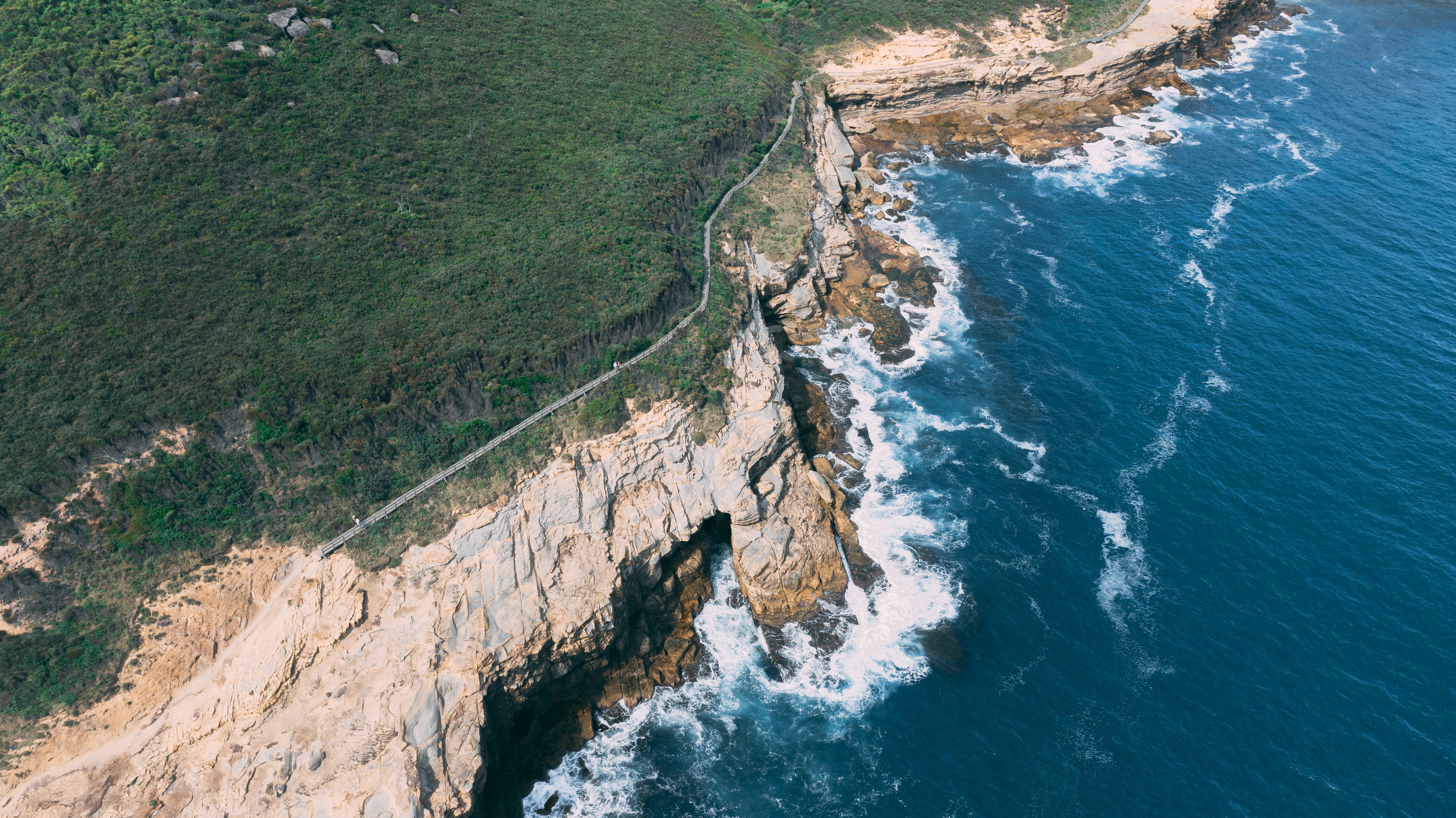 Aerial view of rugged cliffs meeting the vibrant blue ocean, with waves crashing against the rocks.