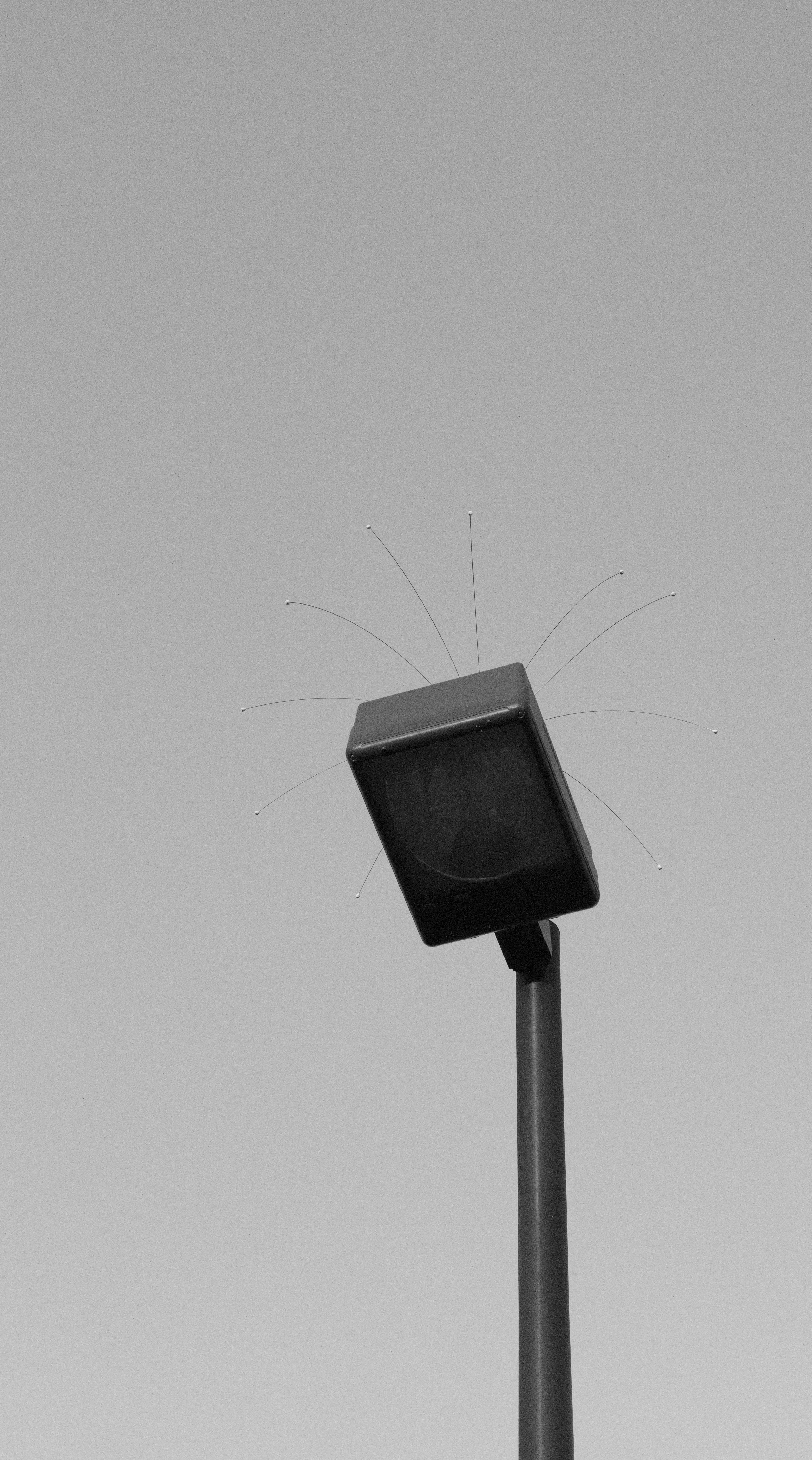 A streetlight stands tall against a clear sky, featuring delicate wires extending from its top. The monochrome palette emphasizes the simplicity of urban design.