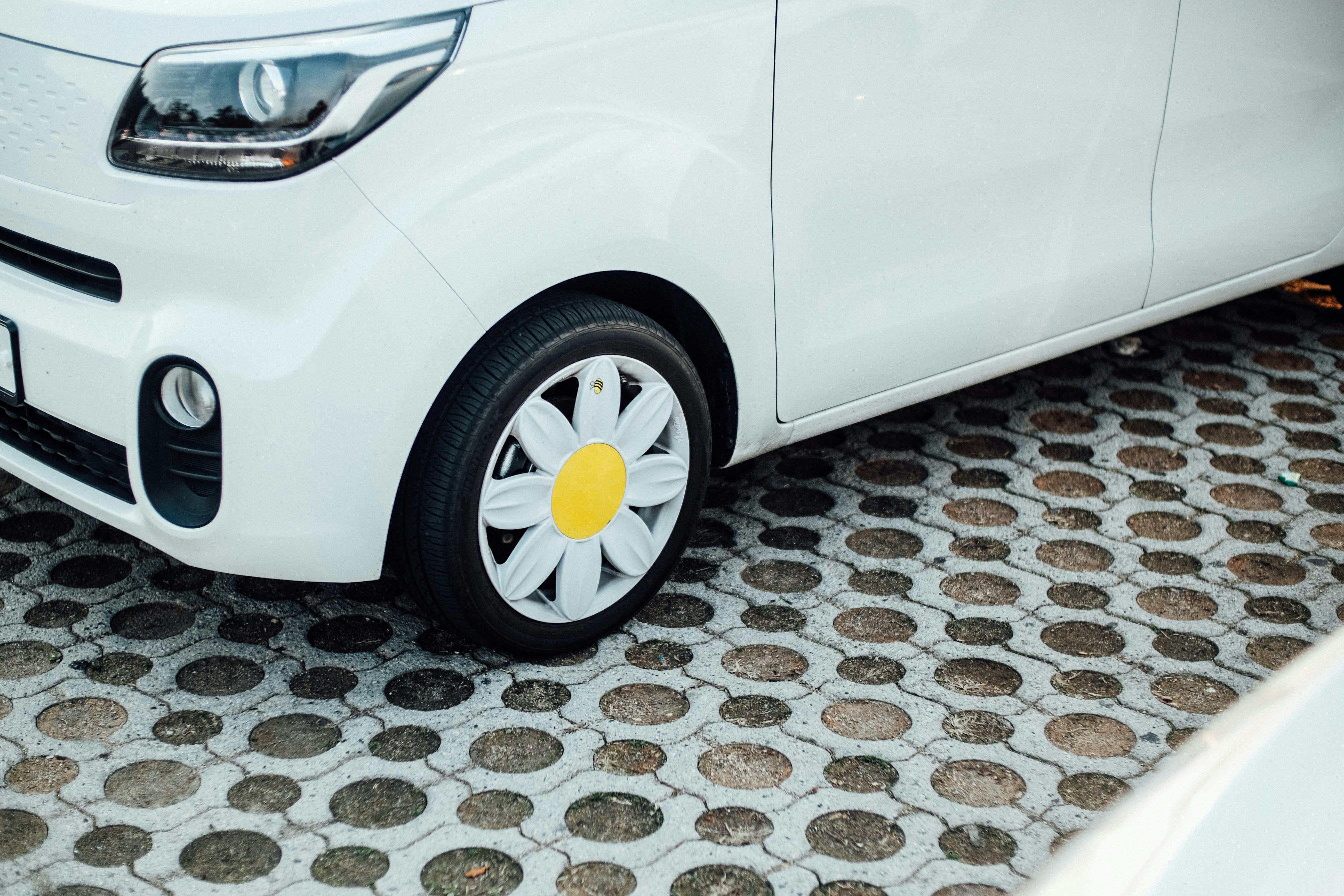 Close-up of a white car's wheel featuring a vibrant yellow hubcap, set against a textured stone pavement.