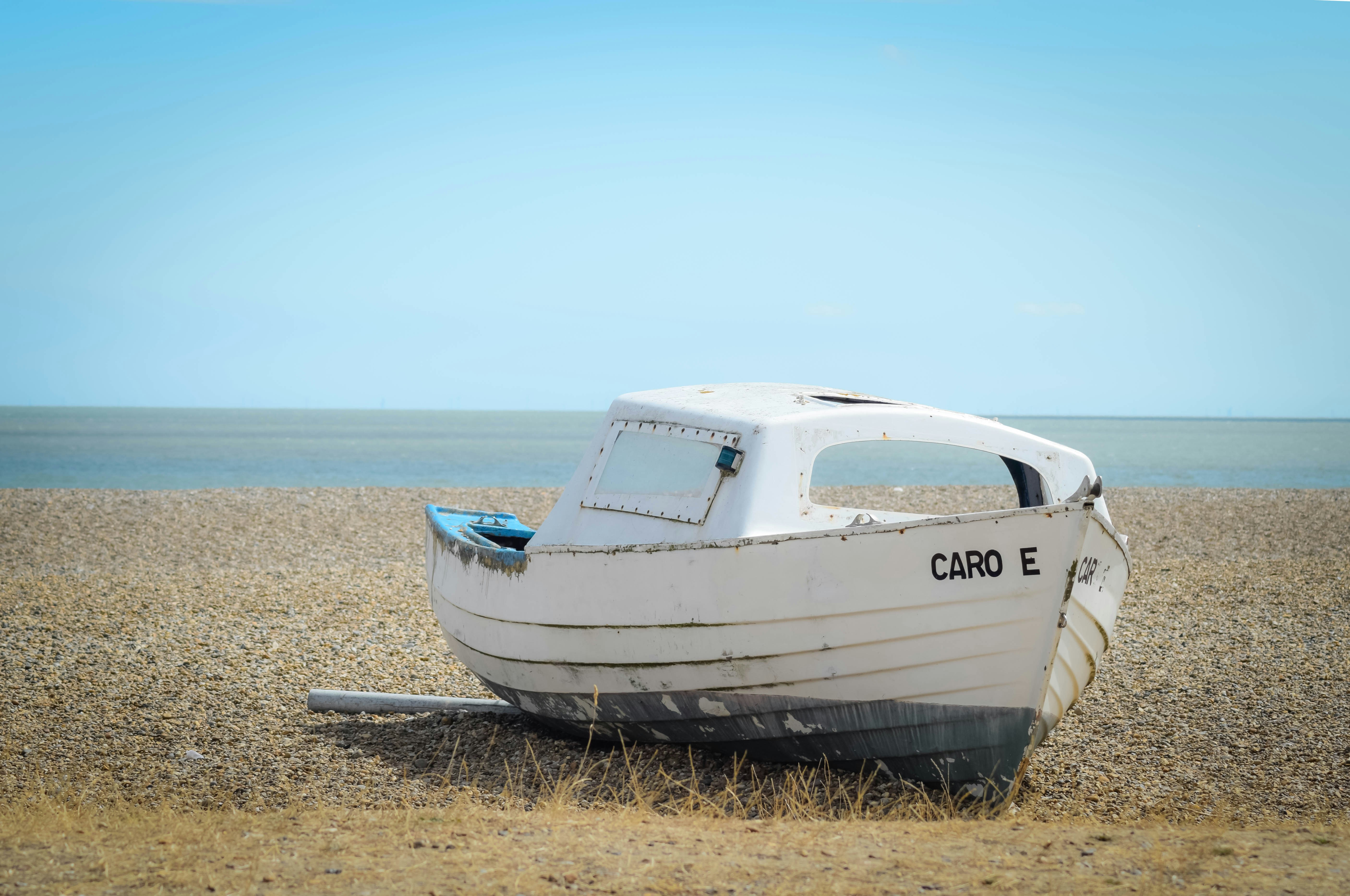 Weathered White Boat Quietly Reposes on Pebble Beach Under a Pale Blue Sky