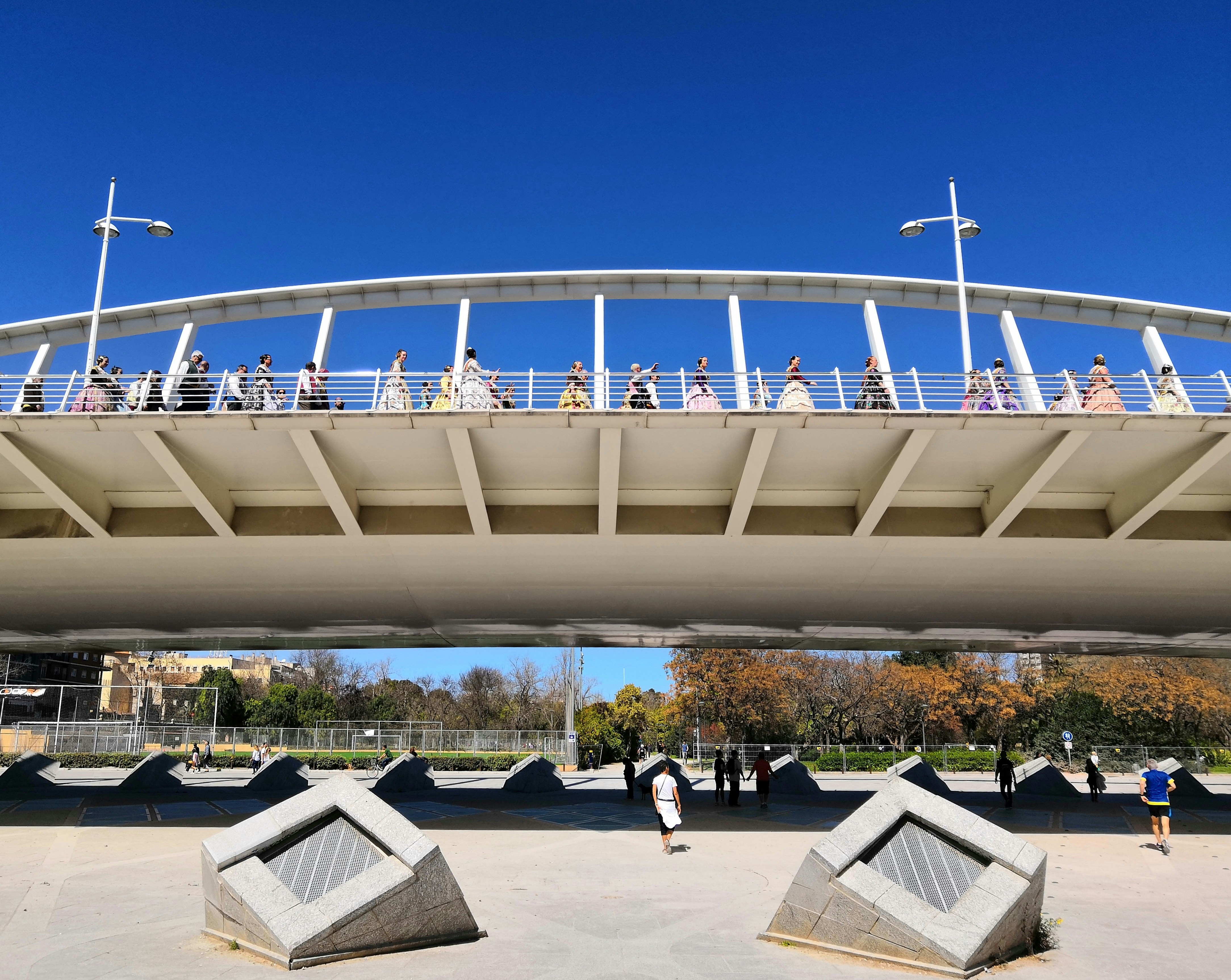 Modern bridge arching over a skate park with vibrant blue sky and geometric shadows.