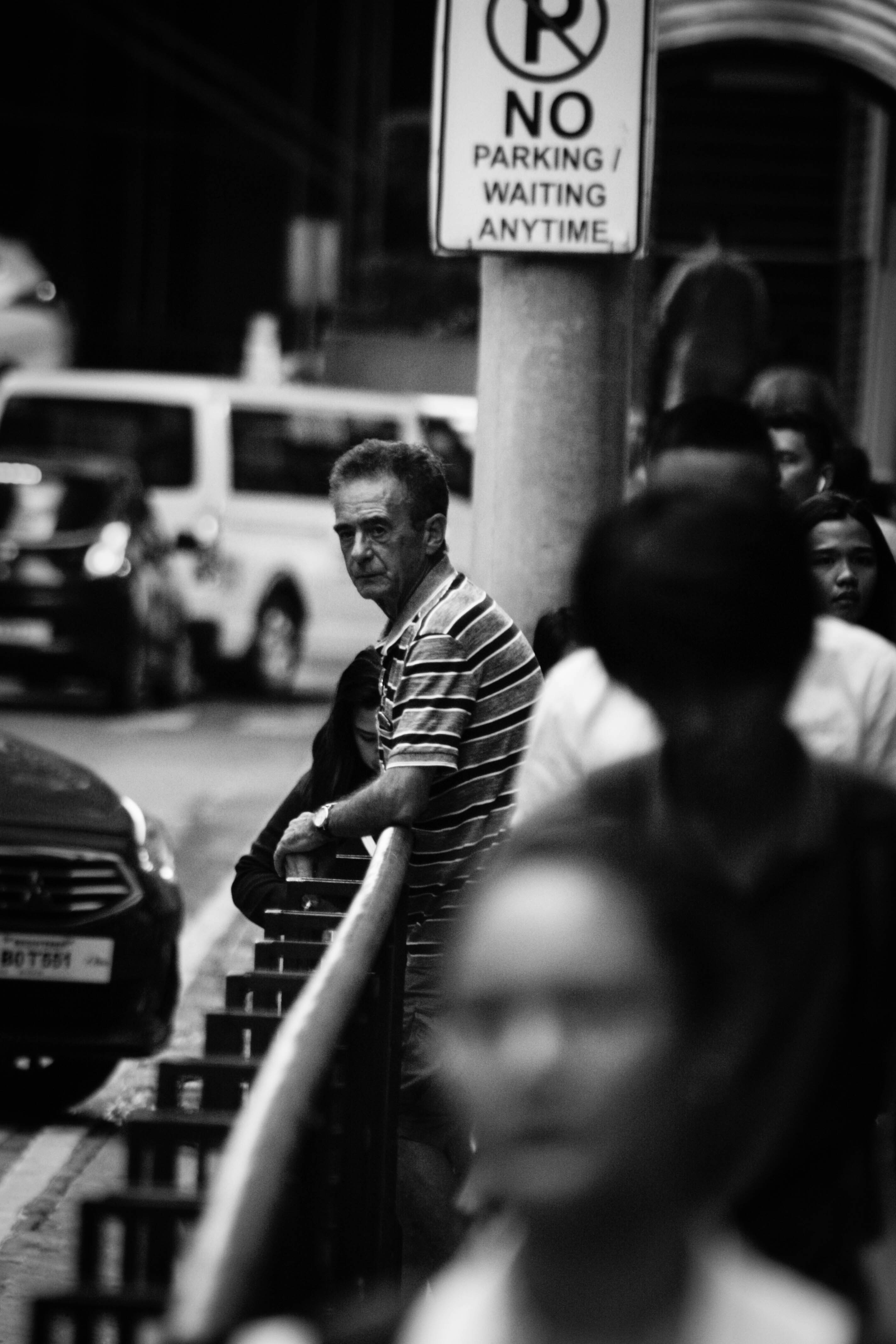 Railside Quiet: Man in a Striped Shirt Anchored in a Moving City