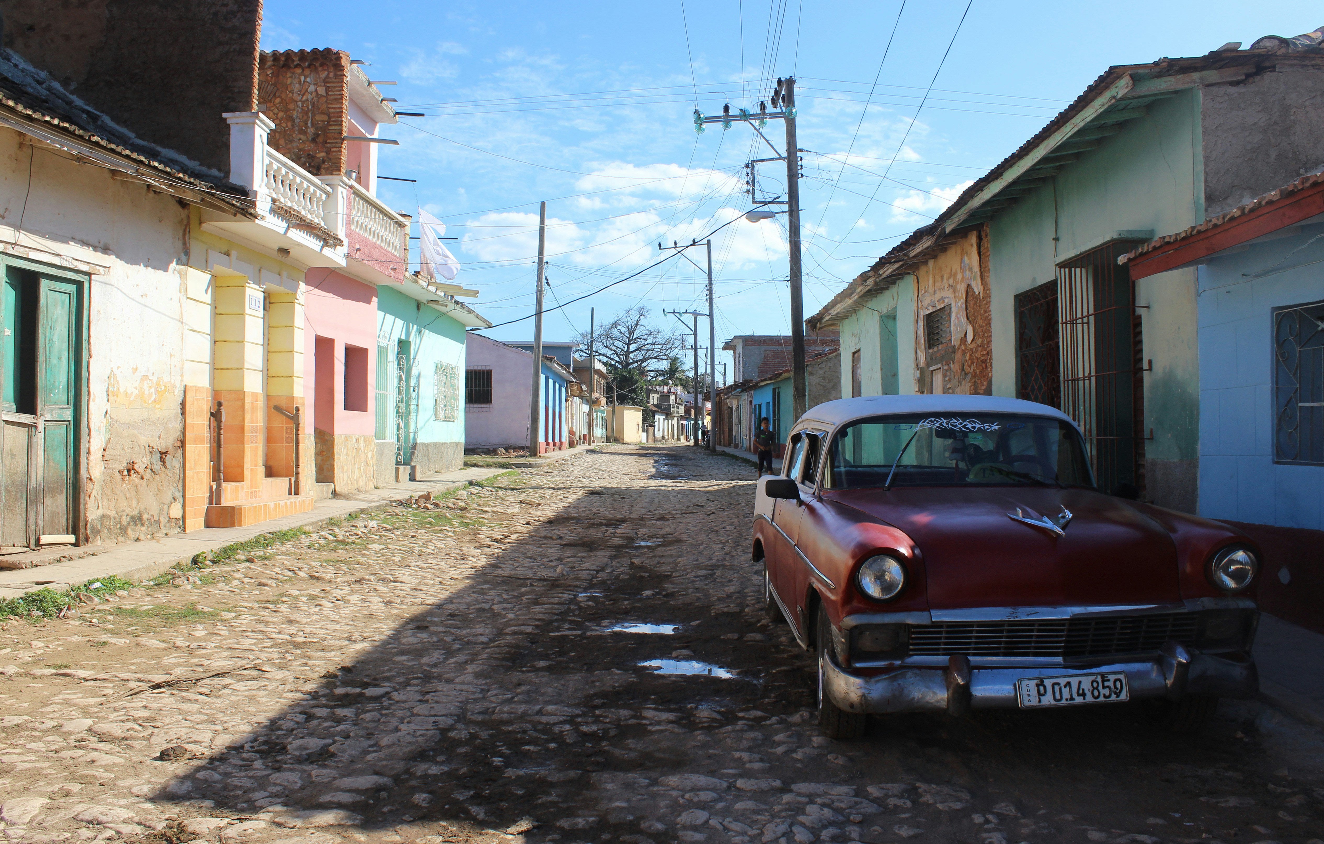 Classic red car parked on a sunlit cobblestone street lined with colorful houses.
