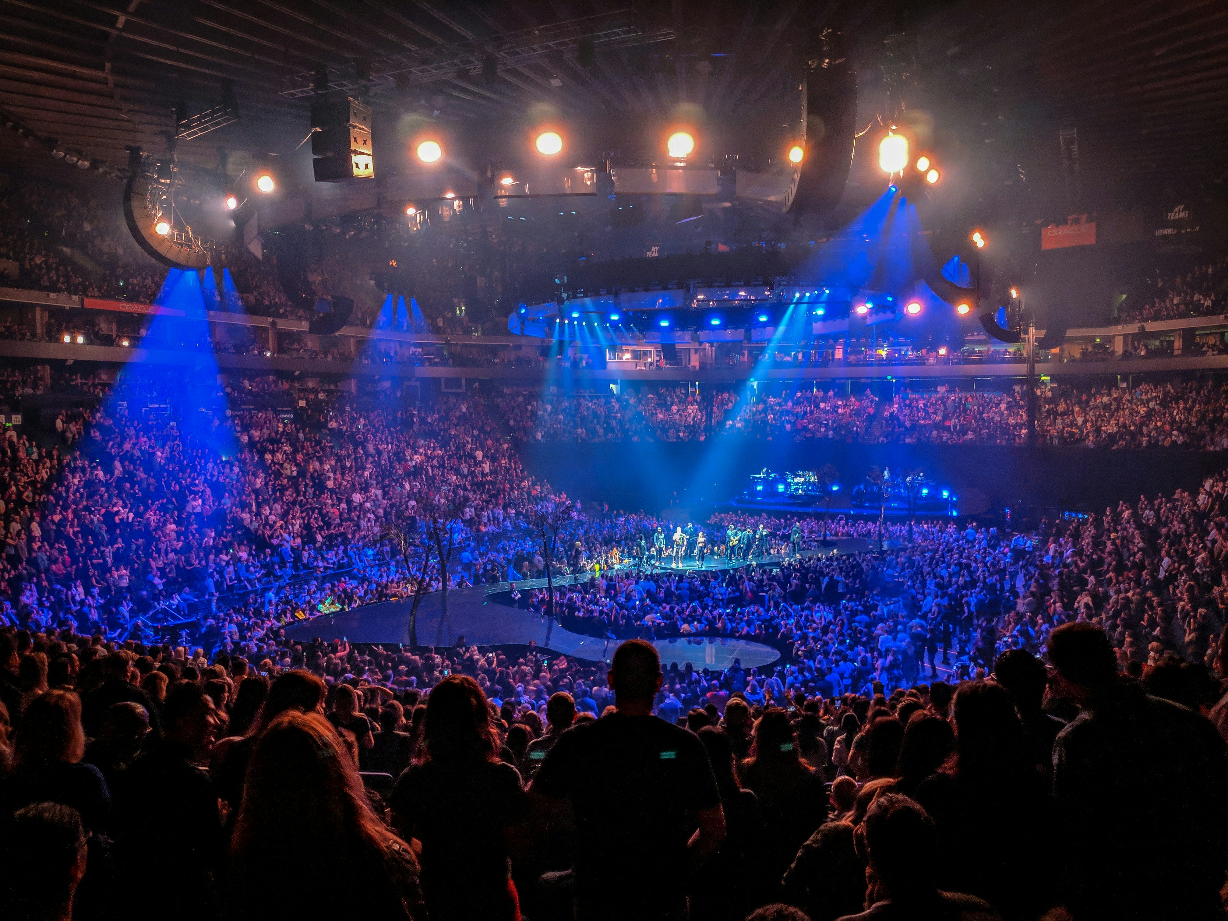 Crowd immersed in a vibrant concert atmosphere, with dramatic blue lighting illuminating the stage and audience. A dynamic scene filled with excitement and anticipation.