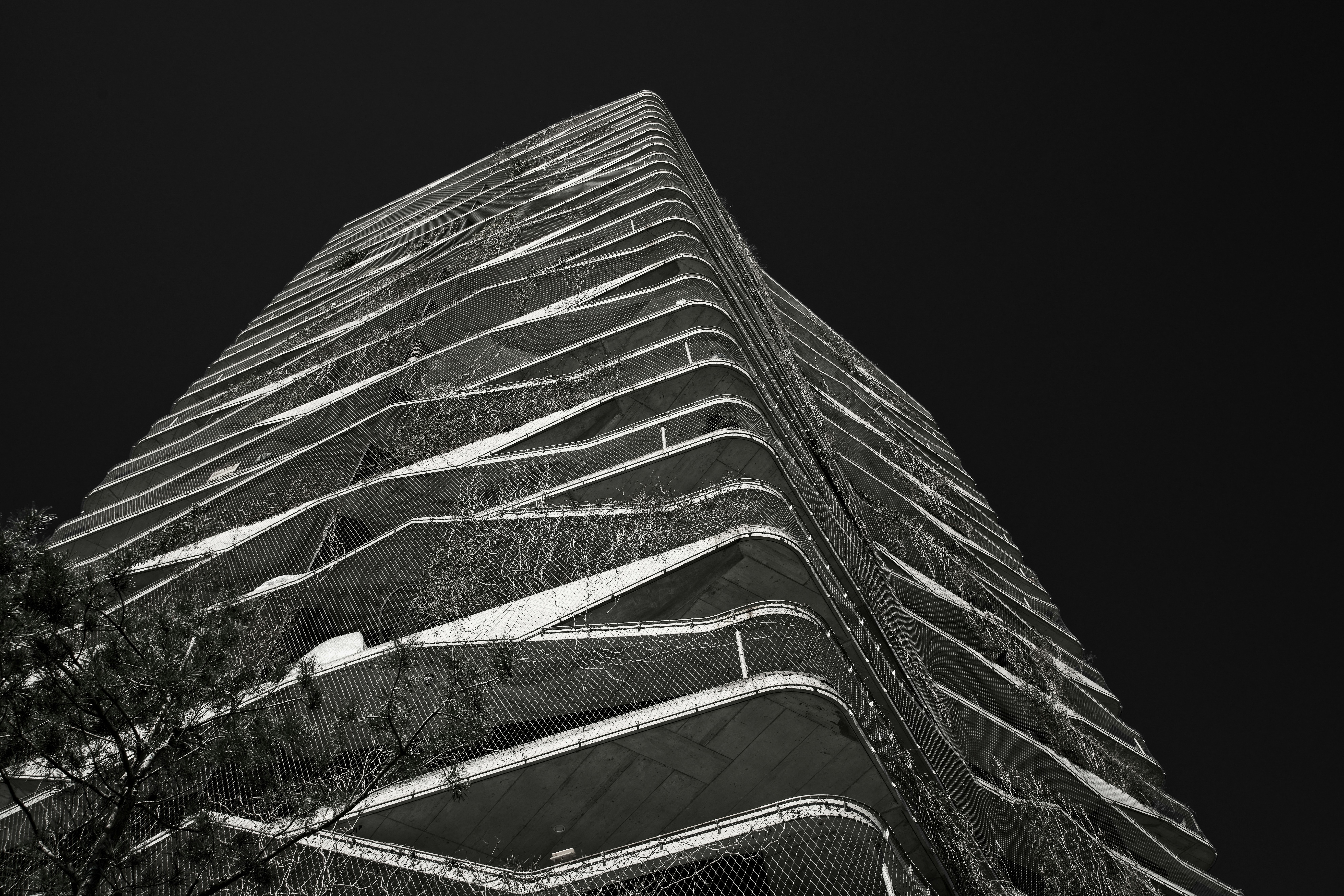 Black and white photo of a towering modern building with curving balconies against a dark sky.