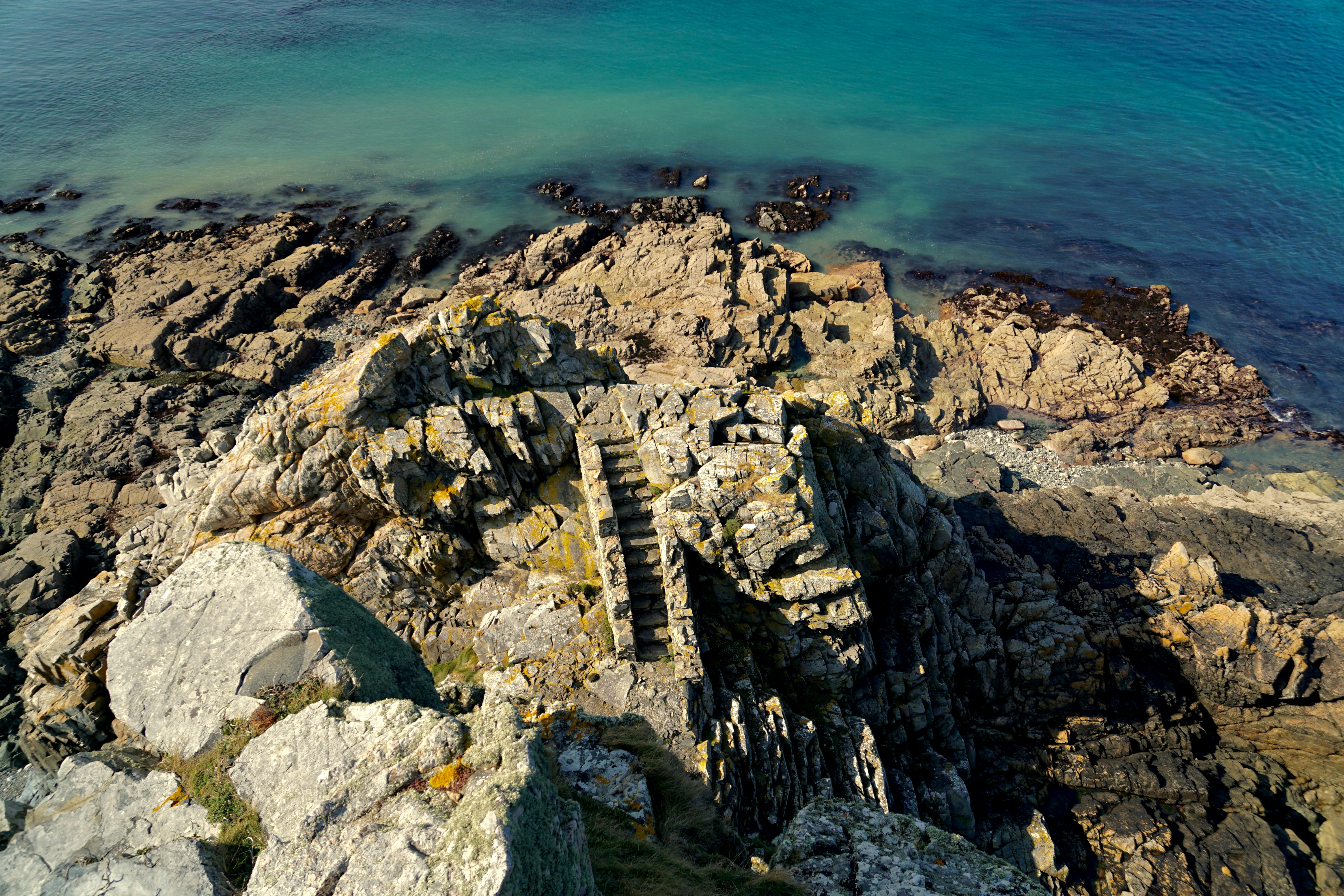 Staircase to the Sea: Aerial Descent Through Weathered Rock Toward Turquoise Waters