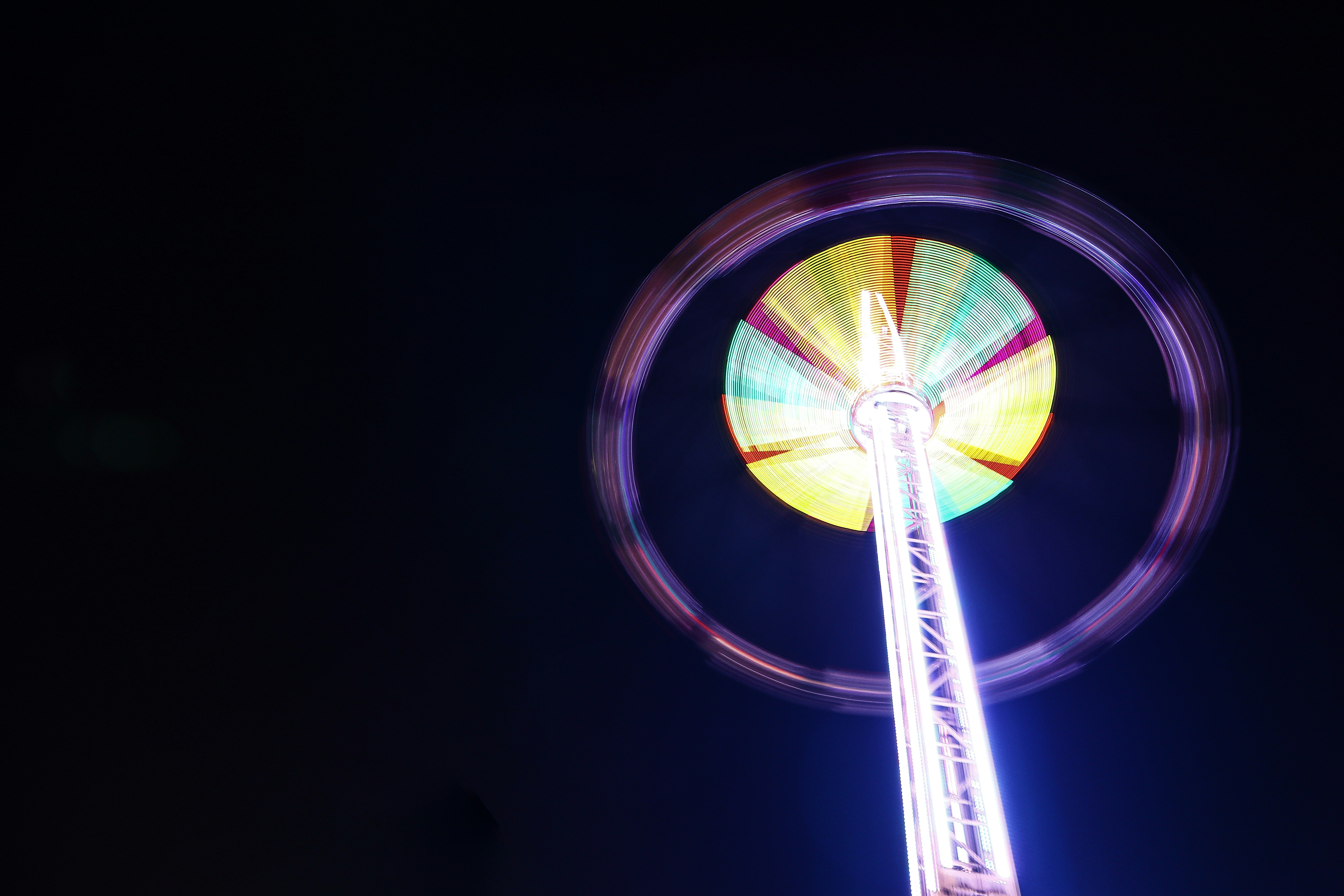 A vibrant spinning amusement ride illuminated by colorful lights against a dark sky.