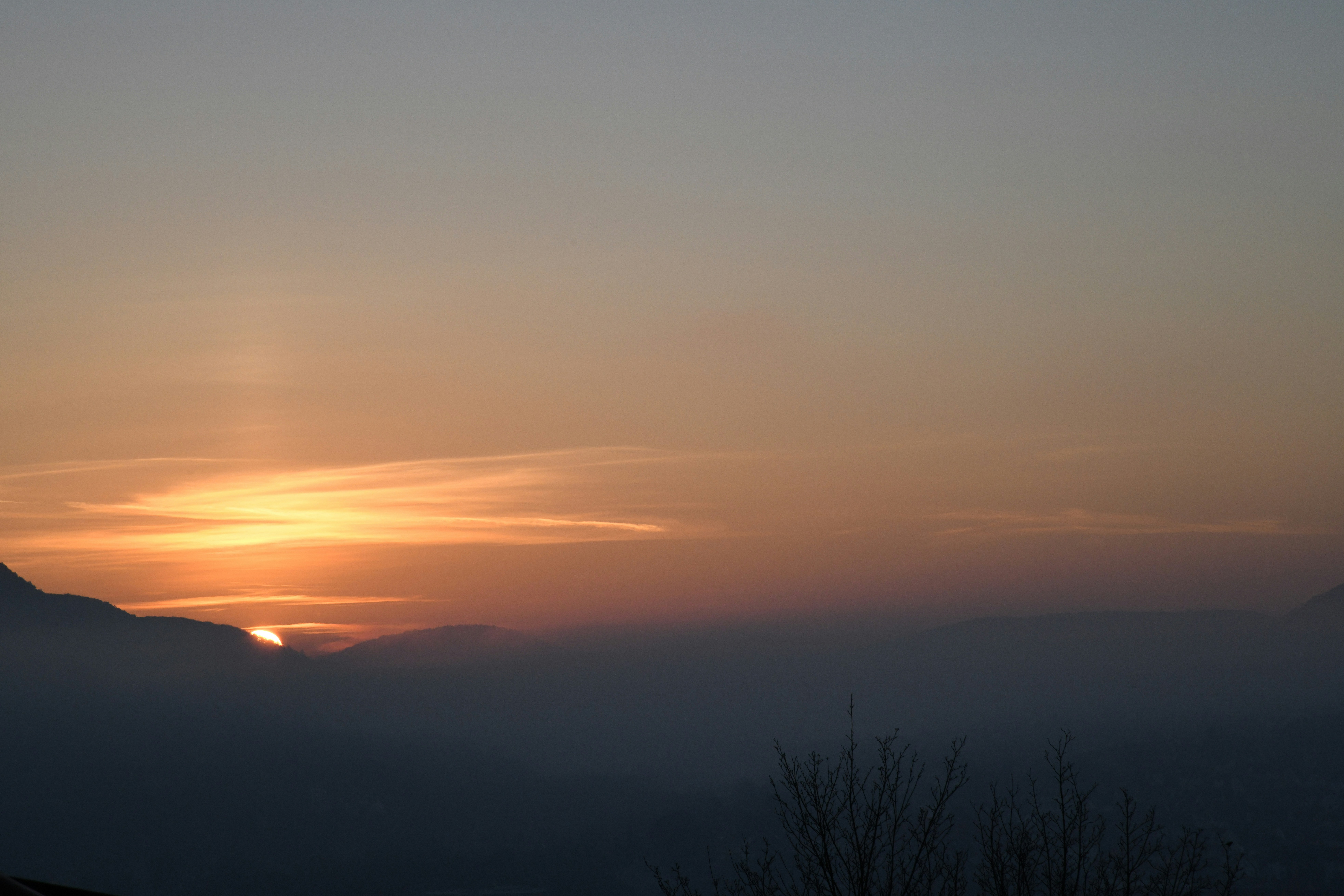 Silhouette of mountains against a sunrise sky with soft orange and blue hues.