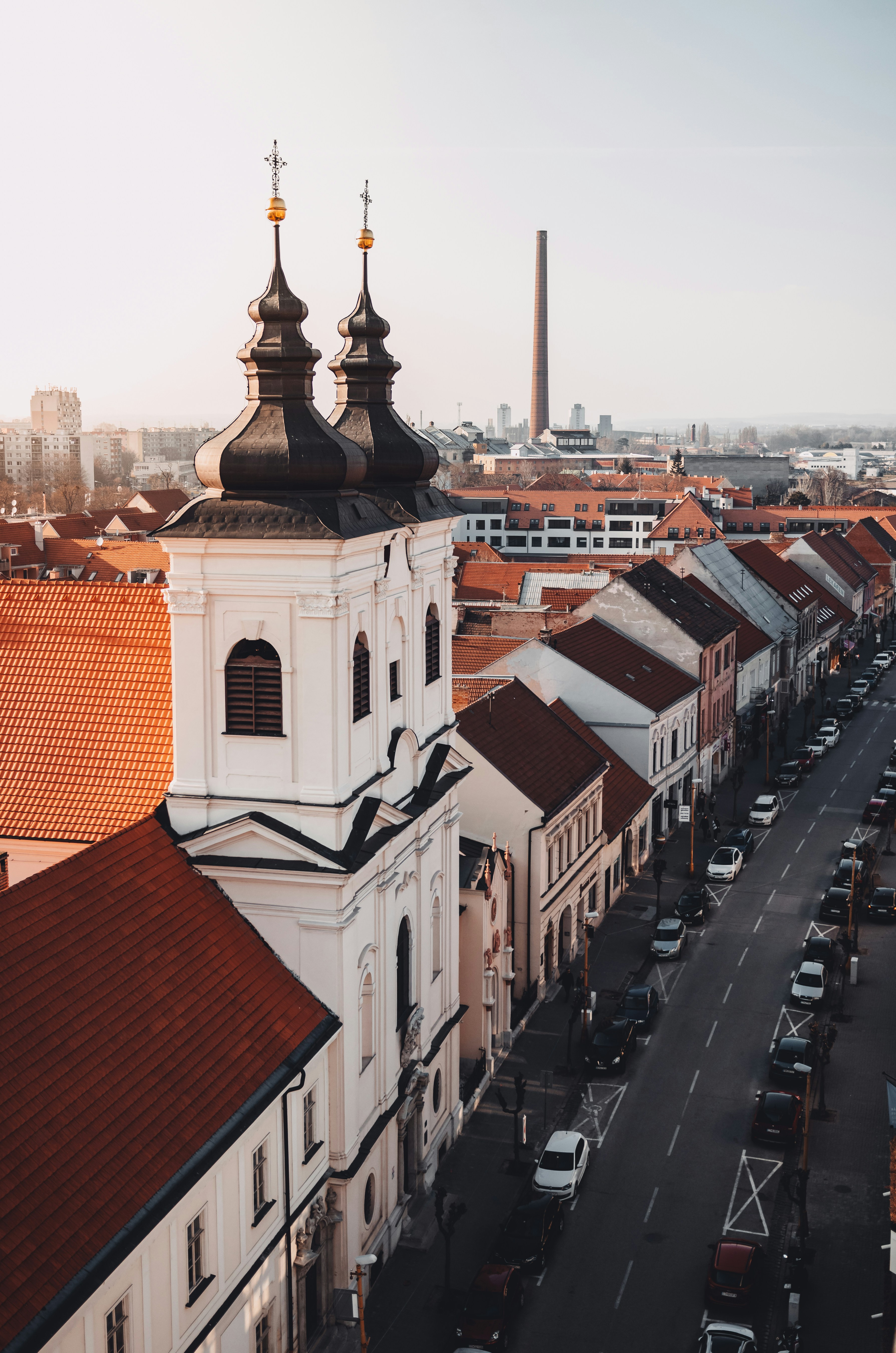 Historic church tower stands prominently above a row of colorful houses, with a smokestack hinting at the city's industrial past.