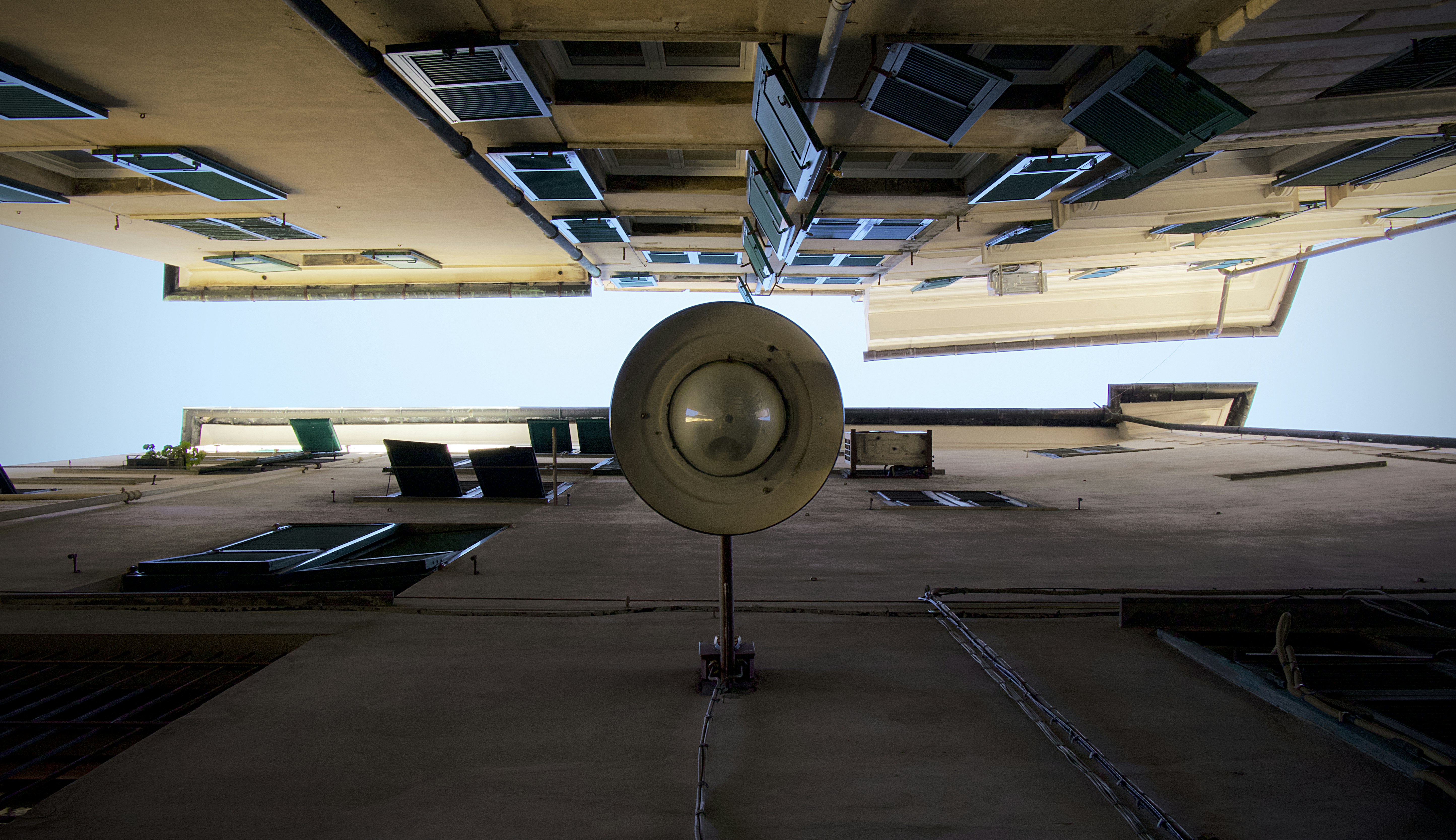 Upward view of a streetlamp surrounded by tall buildings against a clear blue sky.