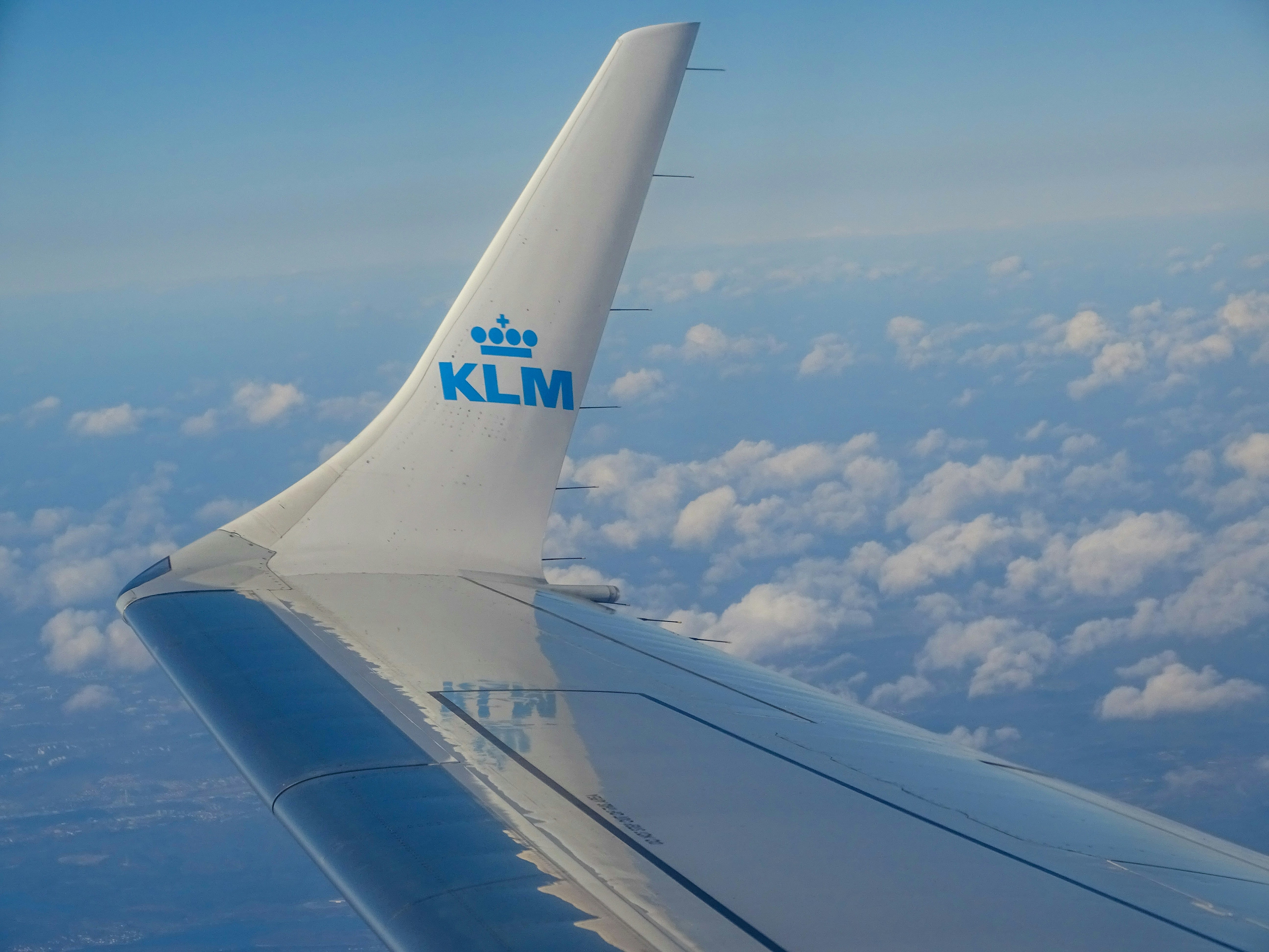 KLM airplane wing glistening in sunlight with clouds below, showcasing the airline's logo prominently.