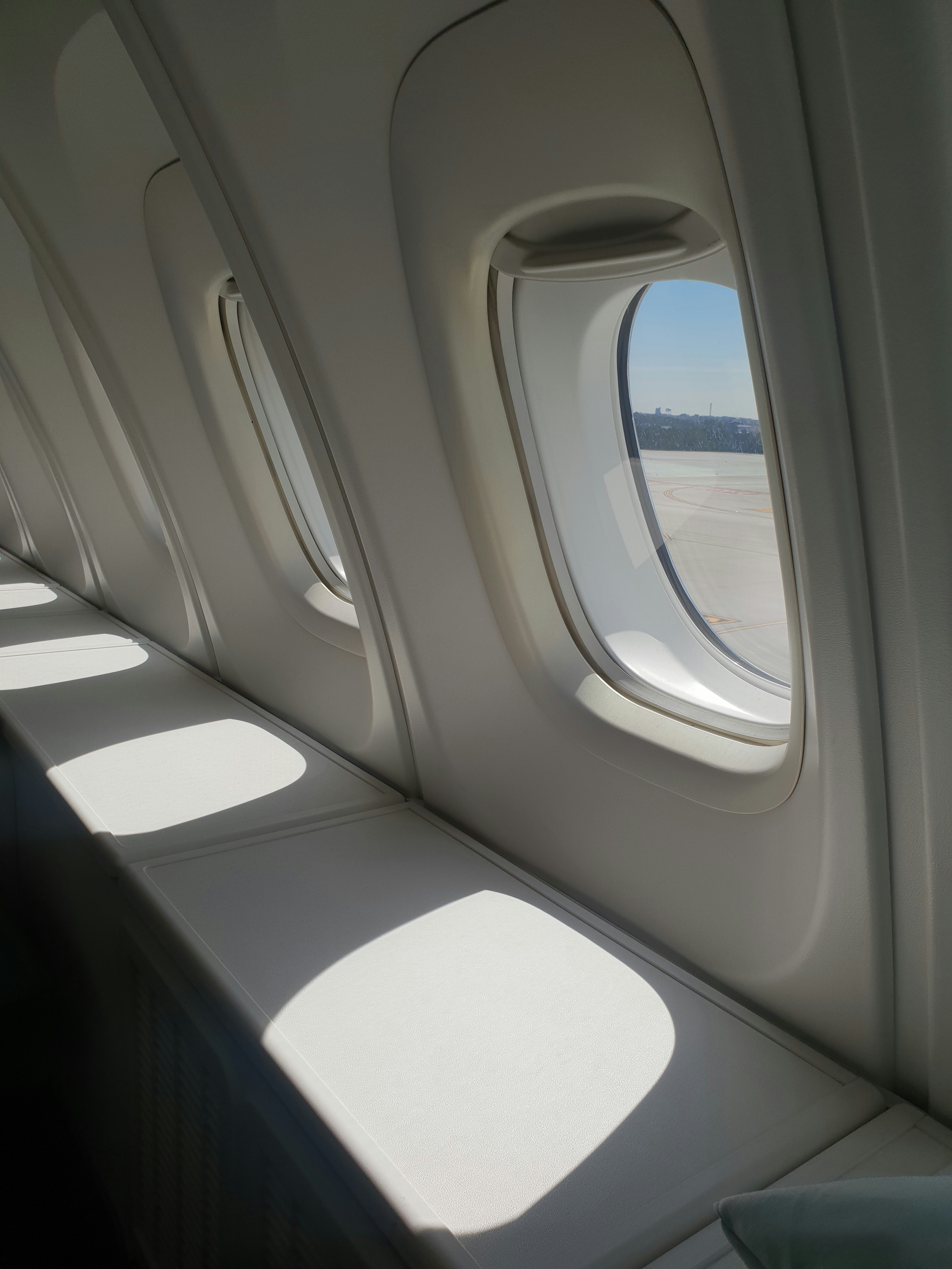 Interior view of an airplane cabin showcasing a row of windows and the sunlight casting shadows on the seat beside them.