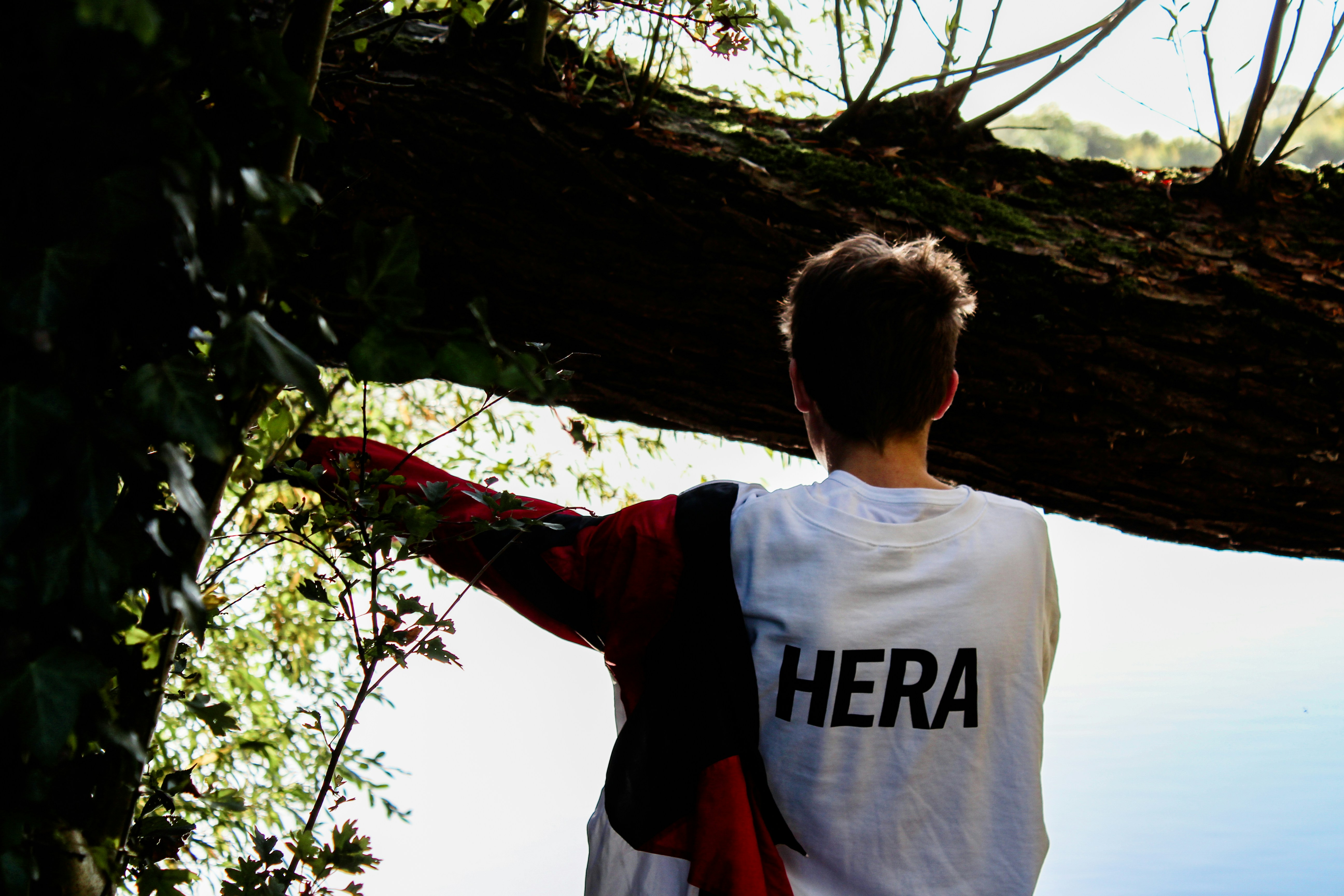 Man wearing white Hera shirt standing near tree outdoors during daytime ...