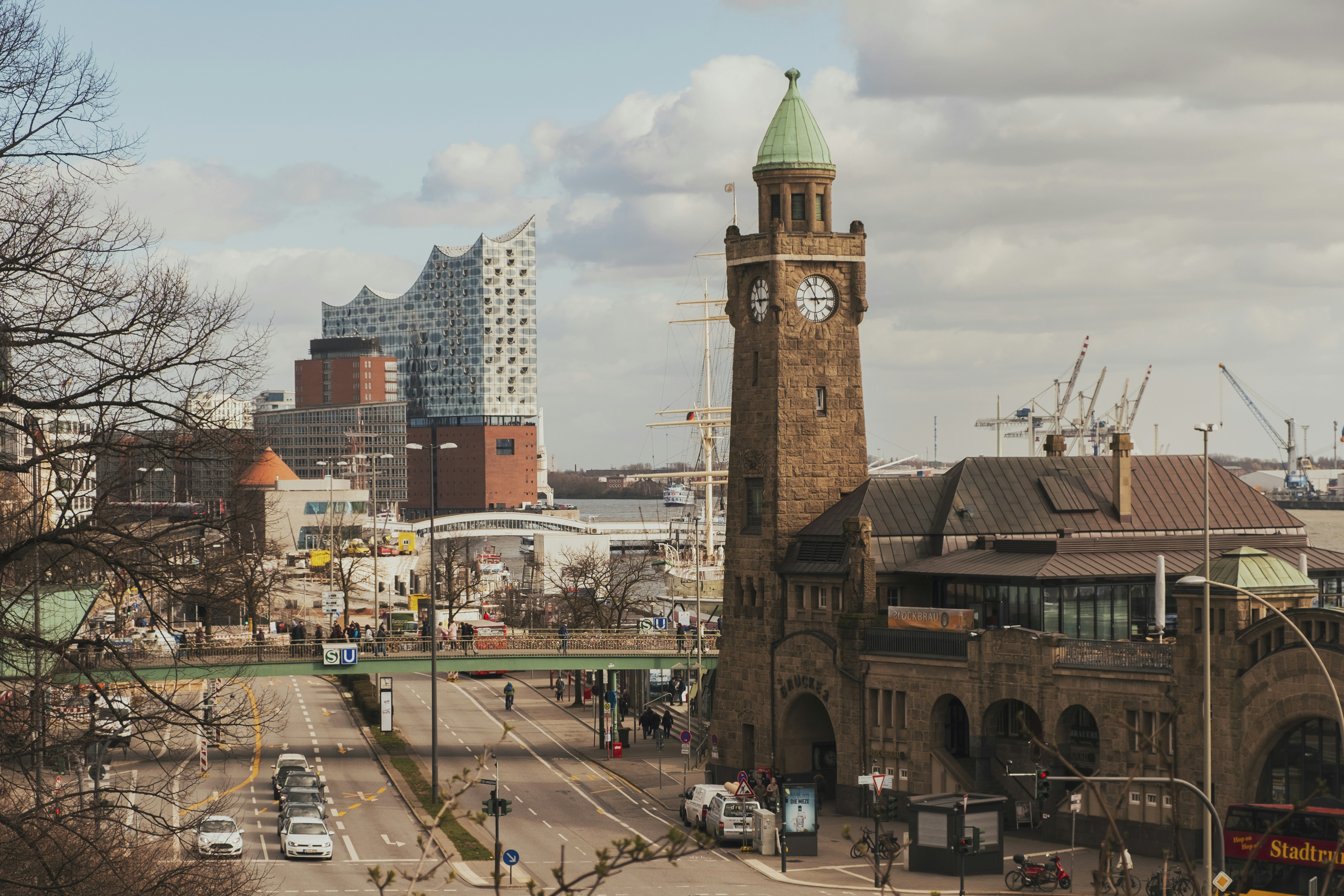Clock tower with a green dome stands amidst bustling cityscape under a partly cloudy sky.