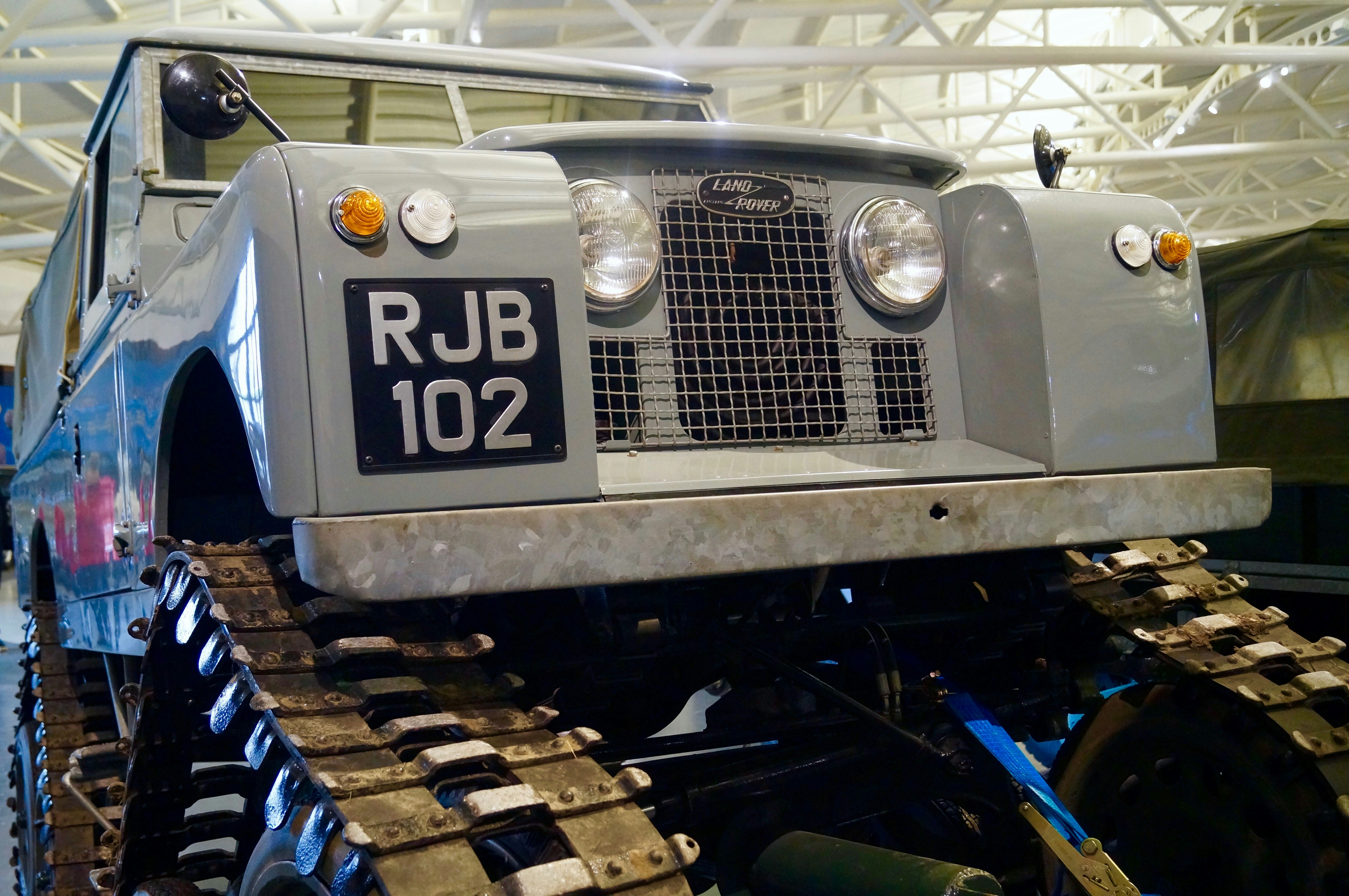 Classic vehicle with tank tracks displayed indoors under industrial lighting.