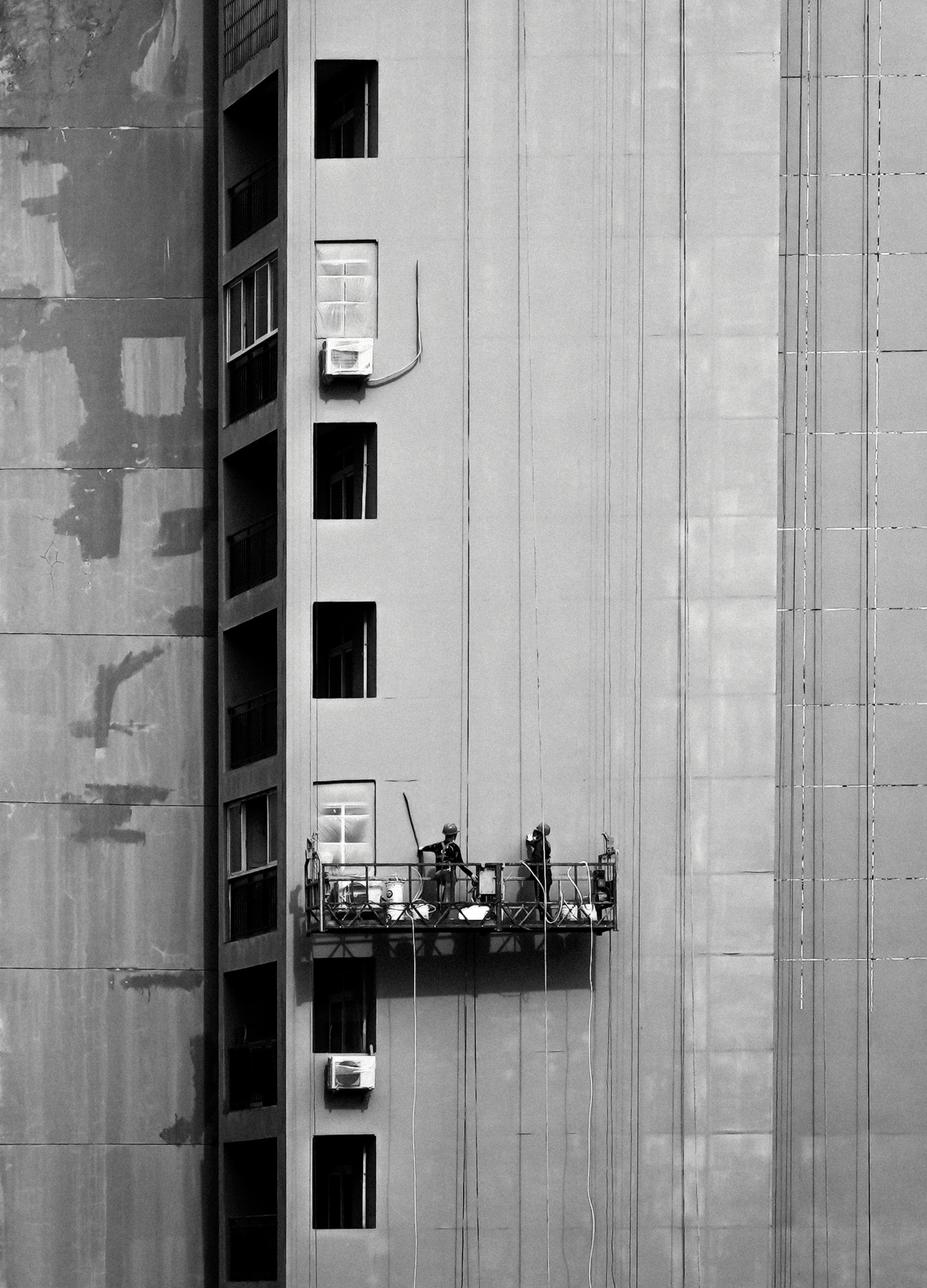 Monochrome Ascent: Workers on a Suspended Platform Against a City Facade