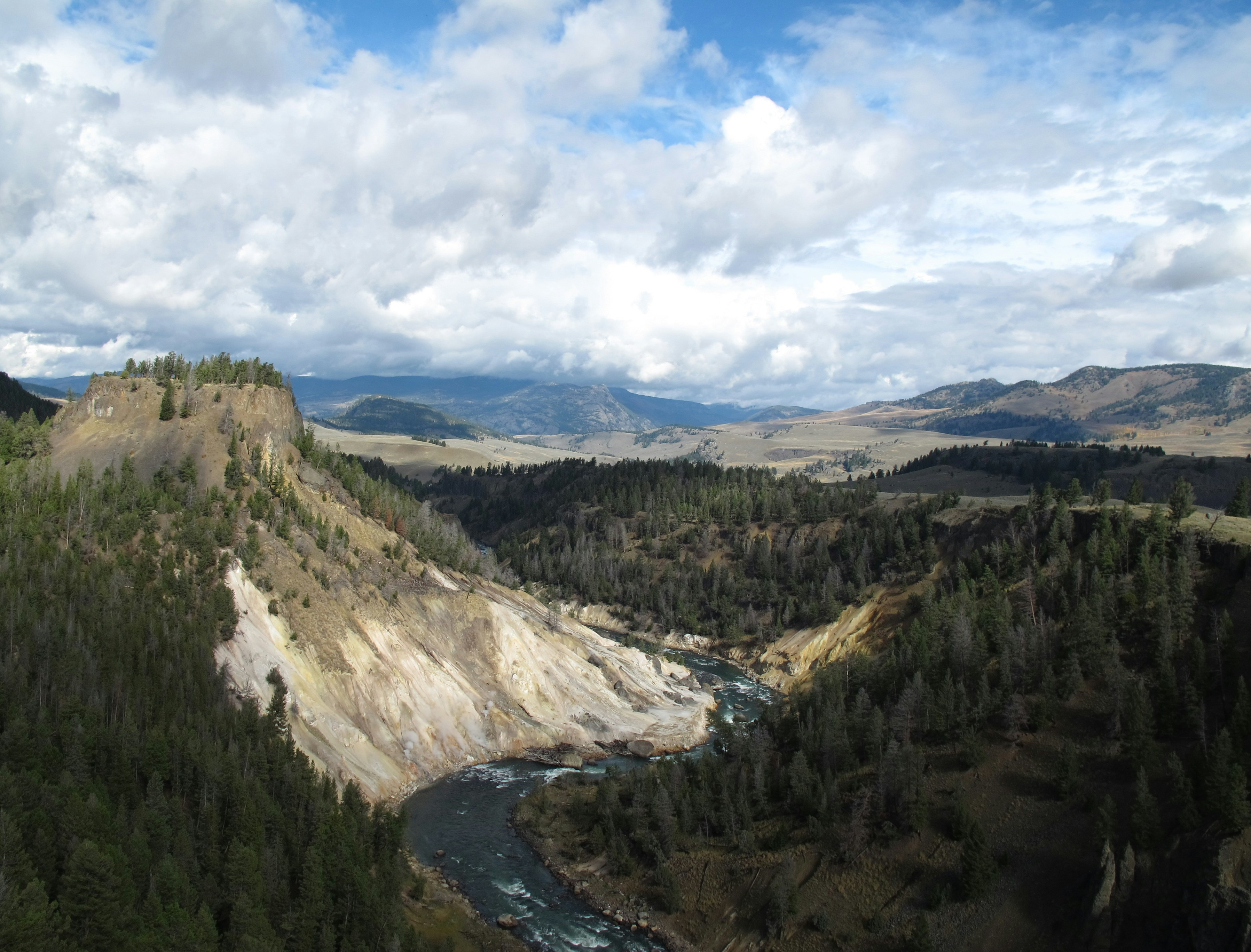 Photograph of a winding river cutting through a forested canyon with rugged cliffs under a partly cloudy sky.