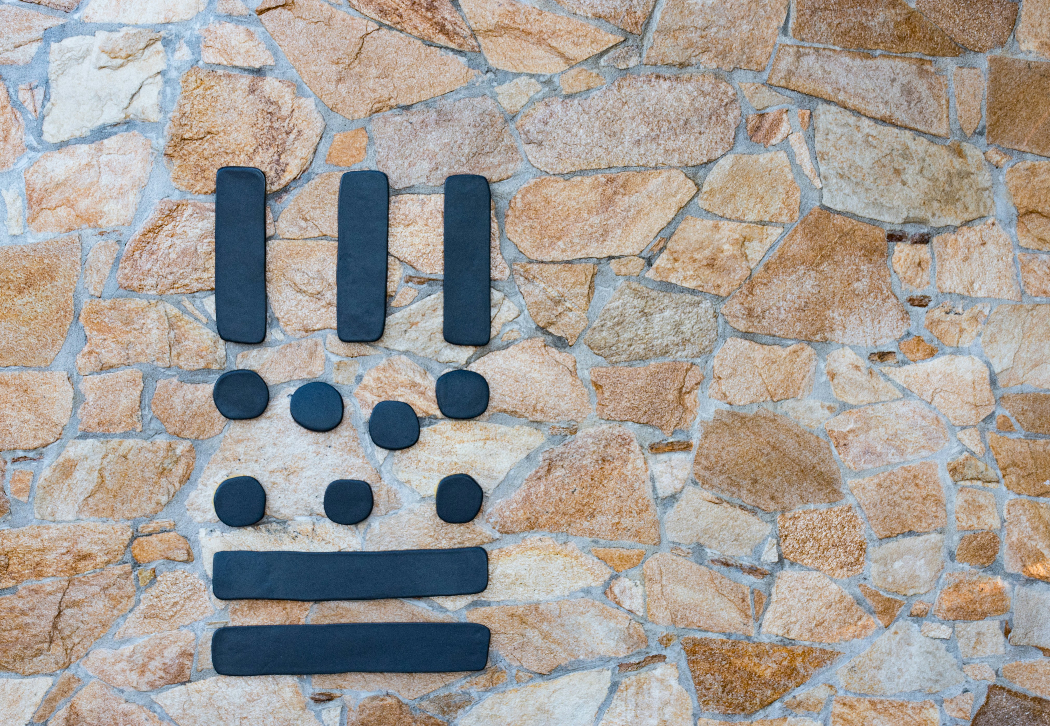 Black geometric shapes arranged against a textured stone wall, creating a striking contrast. The composition emphasizes simplicity and modern design.