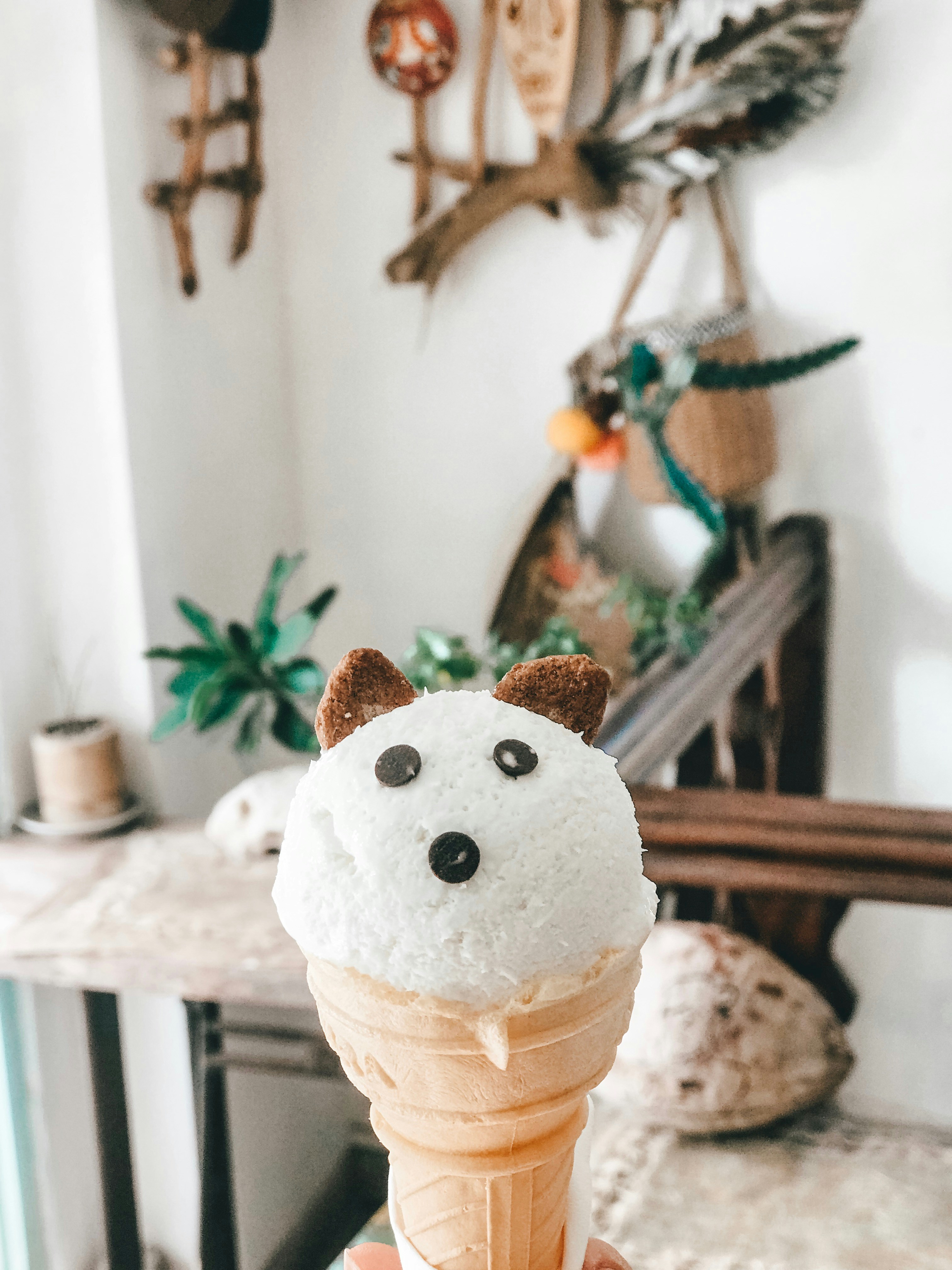 A playful ice cream cone shaped like a dog, featuring chocolate ears and a smiling face, set against a rustic backdrop with greenery and decorative elements.