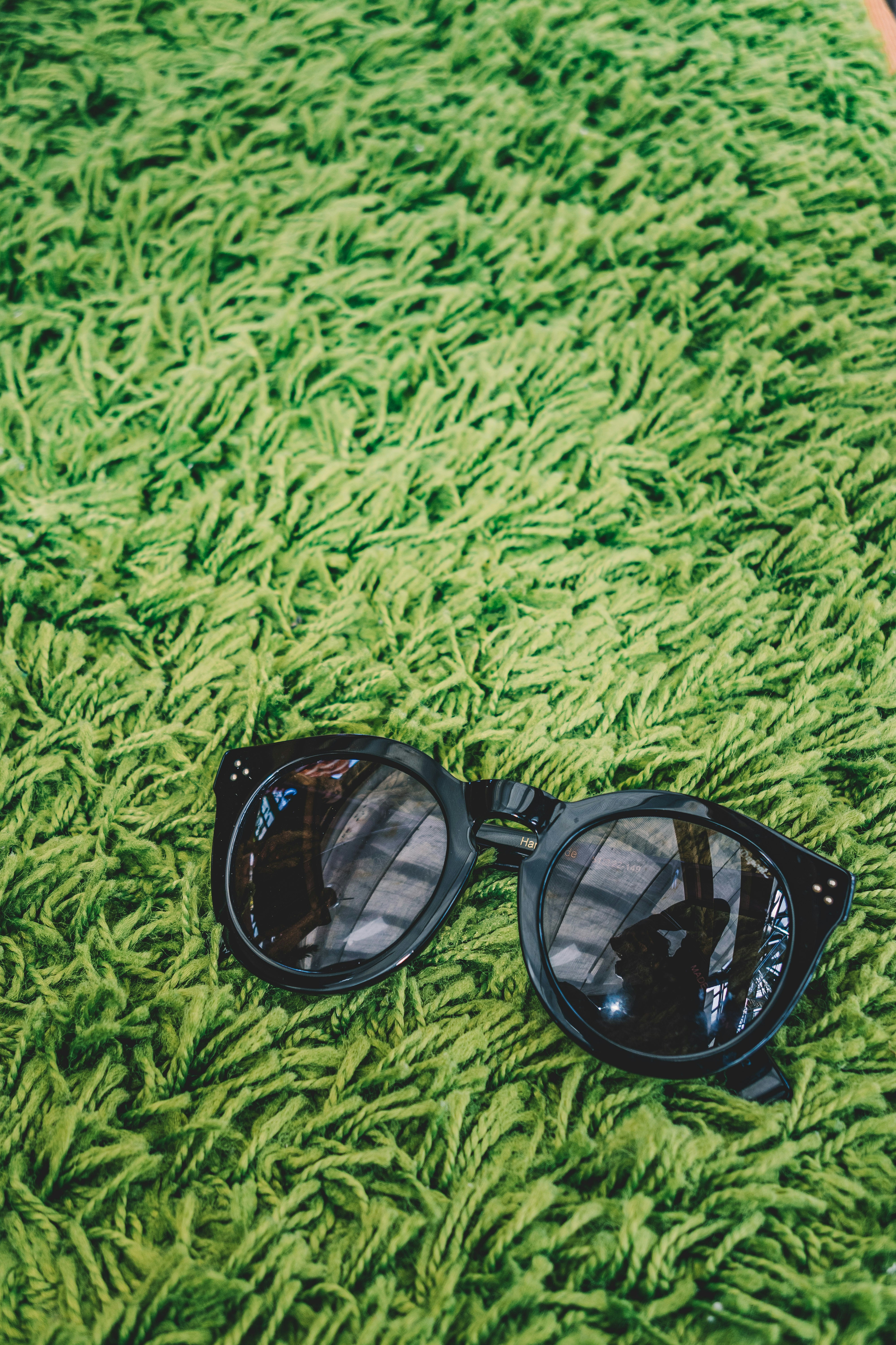 Black sunglasses resting on a vibrant green textured surface.