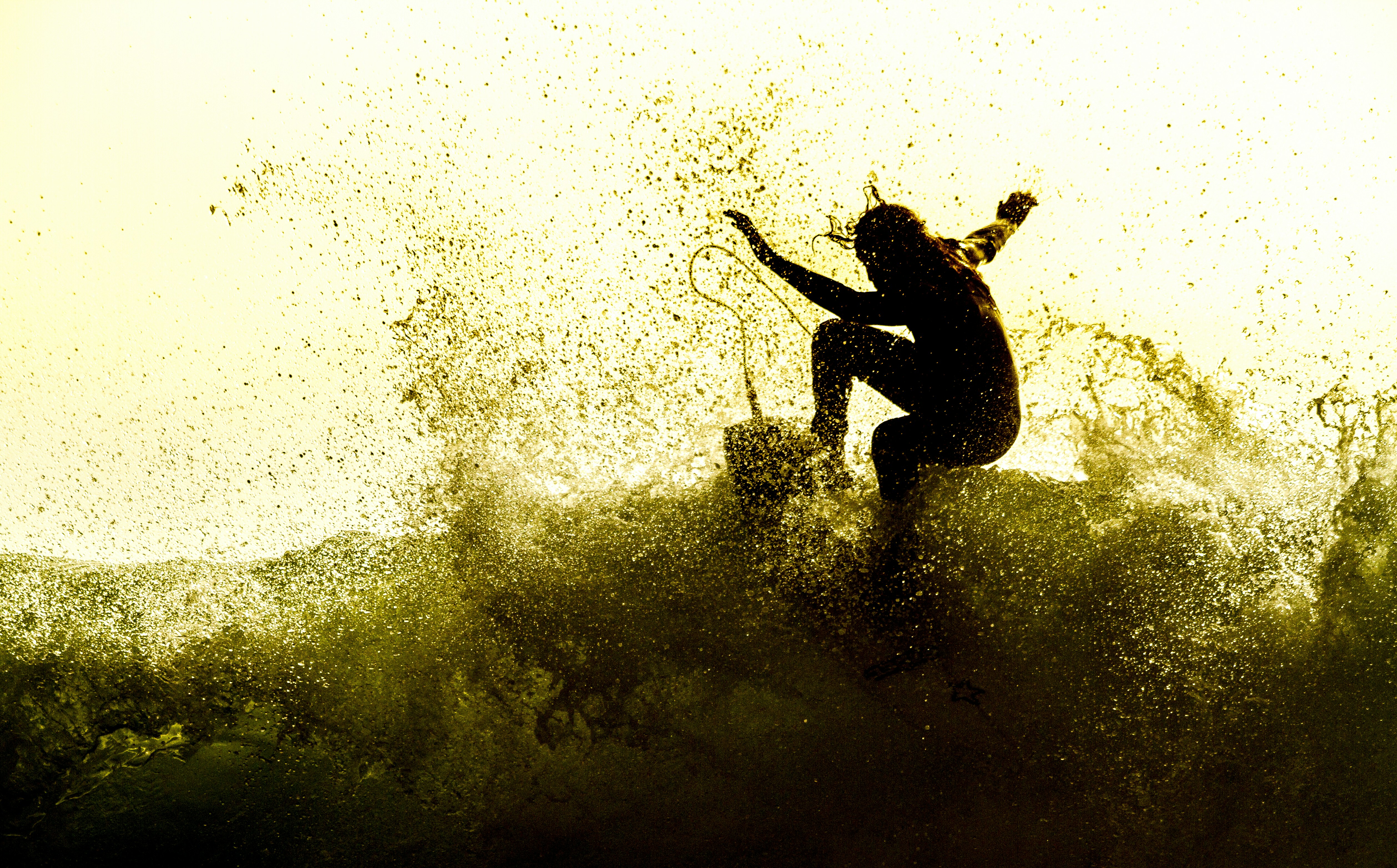 Silhouetted surfer riding a wave with dramatic spray under a golden sky.