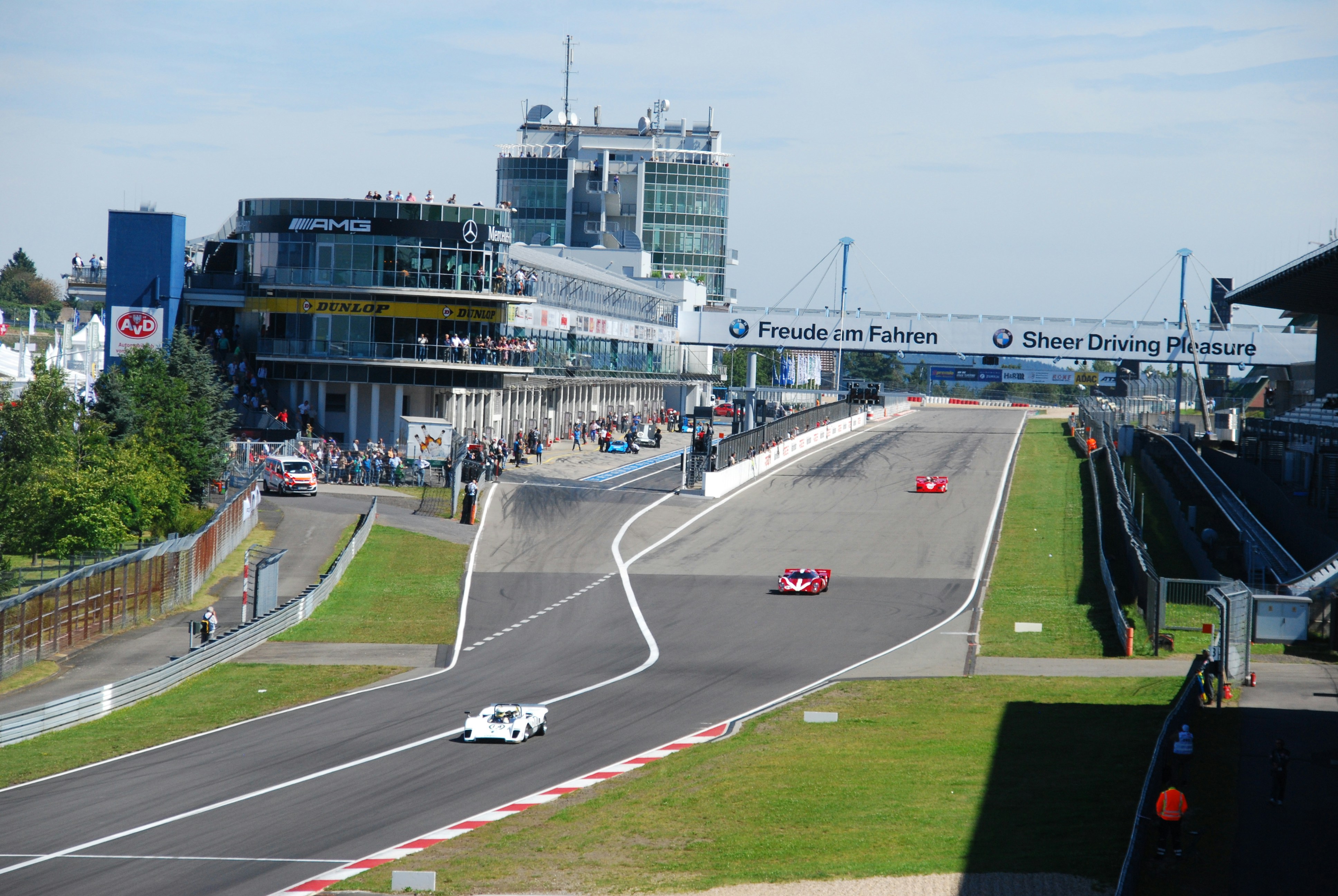 Race cars navigate a winding track with grandstands filled with spectators in the background. The scene captures the excitement of motorsport in a vibrant setting.