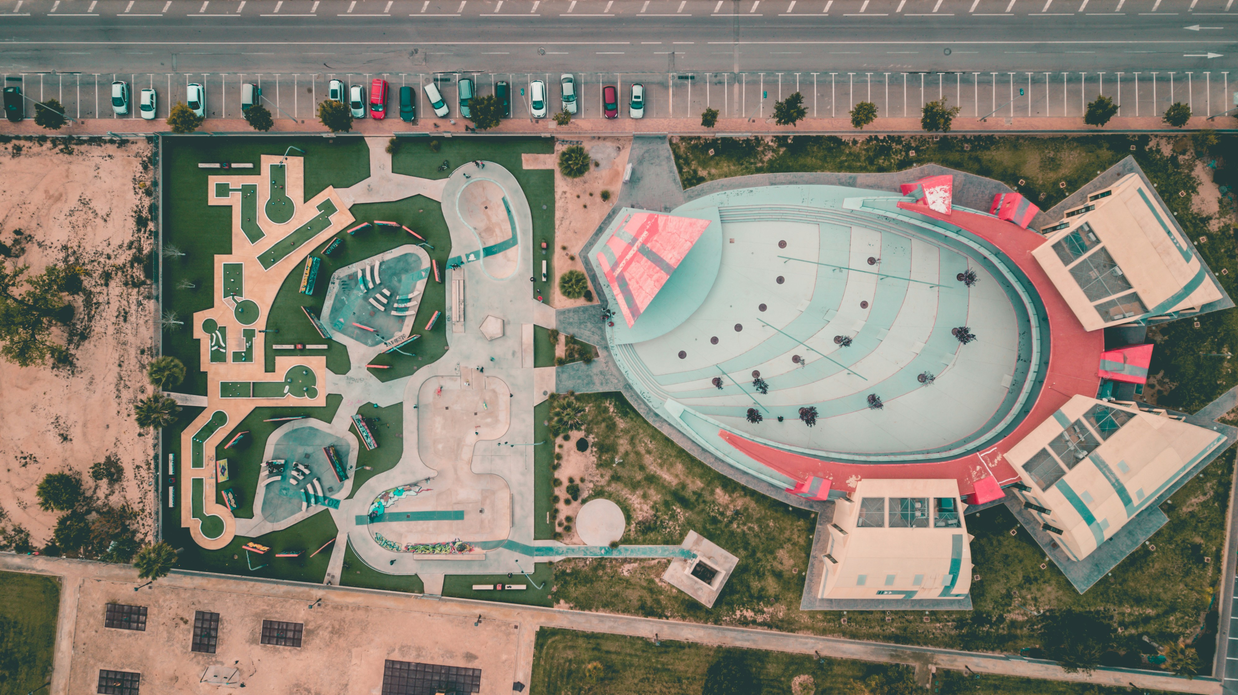 Aerial view of a skatepark and swimming pool complex with geometric design elements and surrounding greenery.