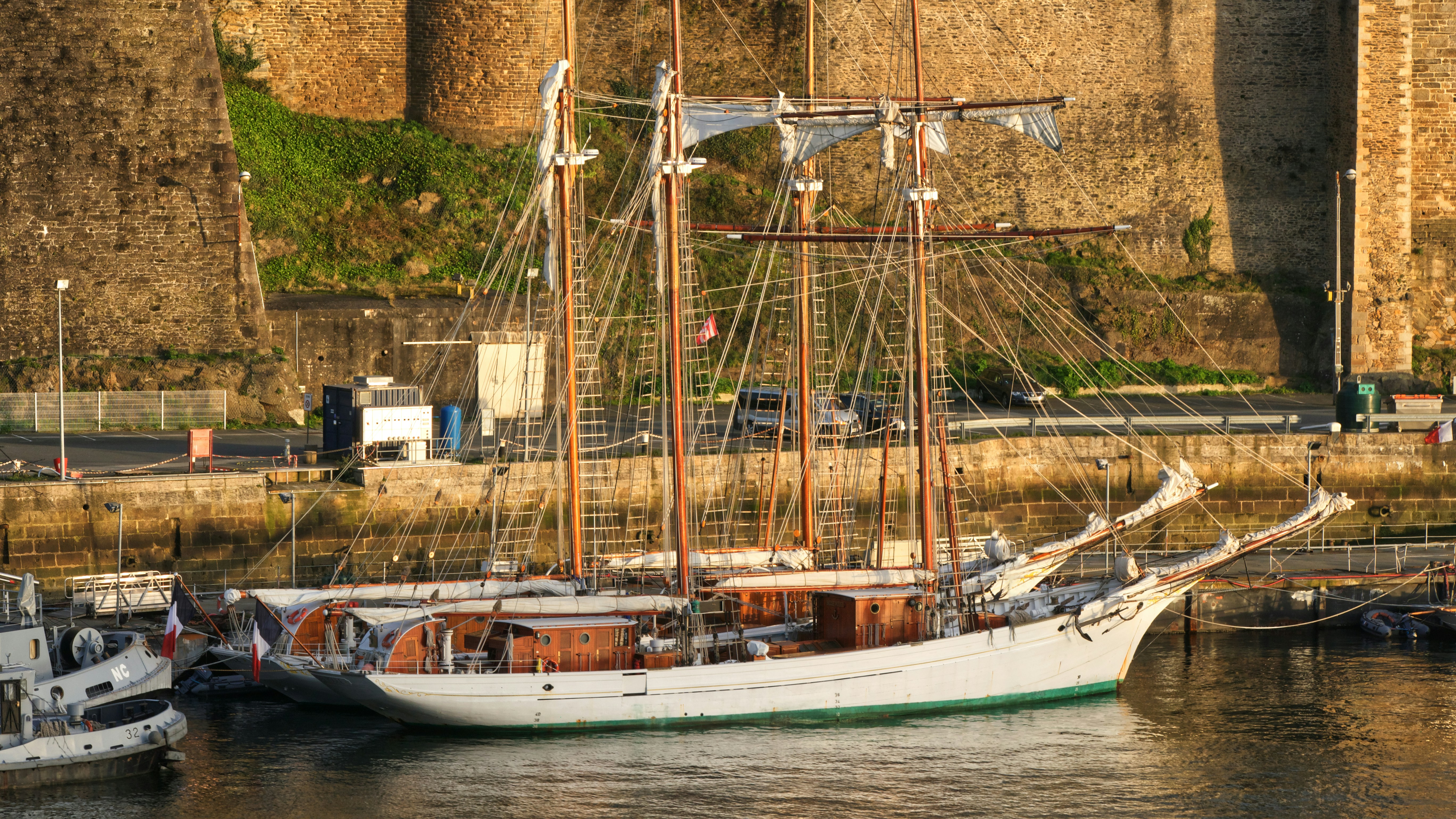 Sailing ships moored beside a historic stone wall under warm light.