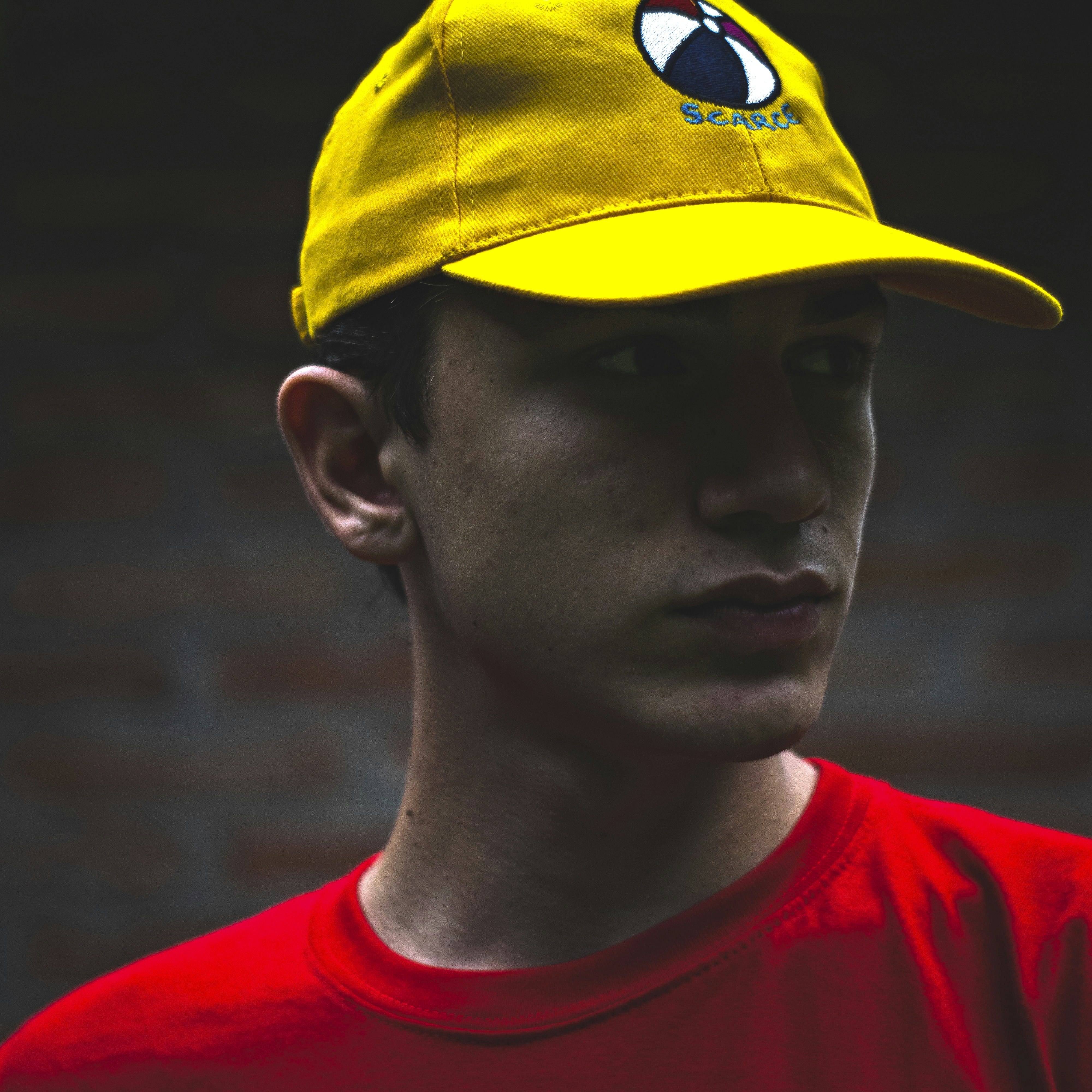 Yellow cap, red shirt, and shadowed gaze: a quiet portrait in brick light