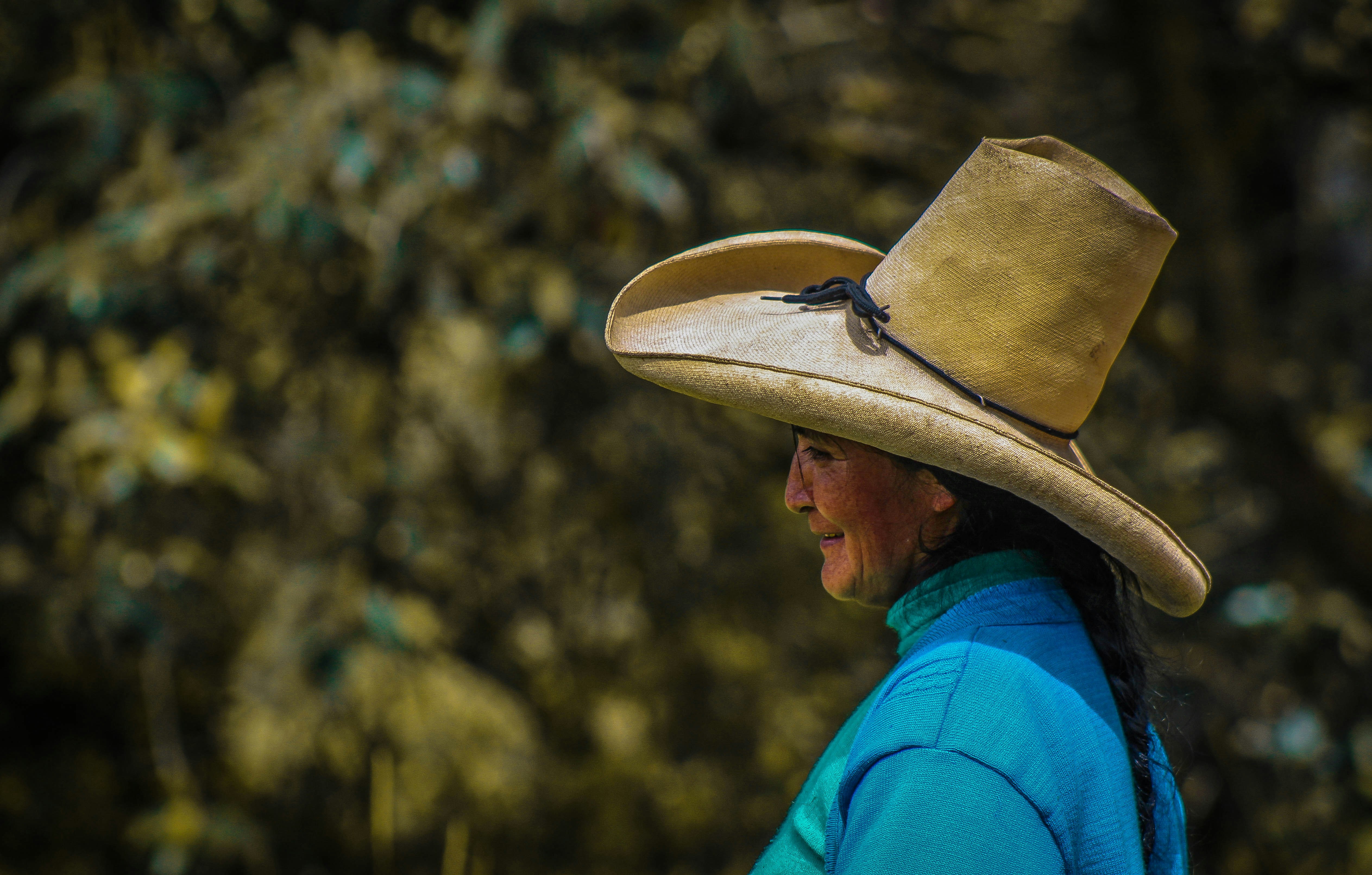 Person in traditional attire with a large hat against a blurred natural backdrop.