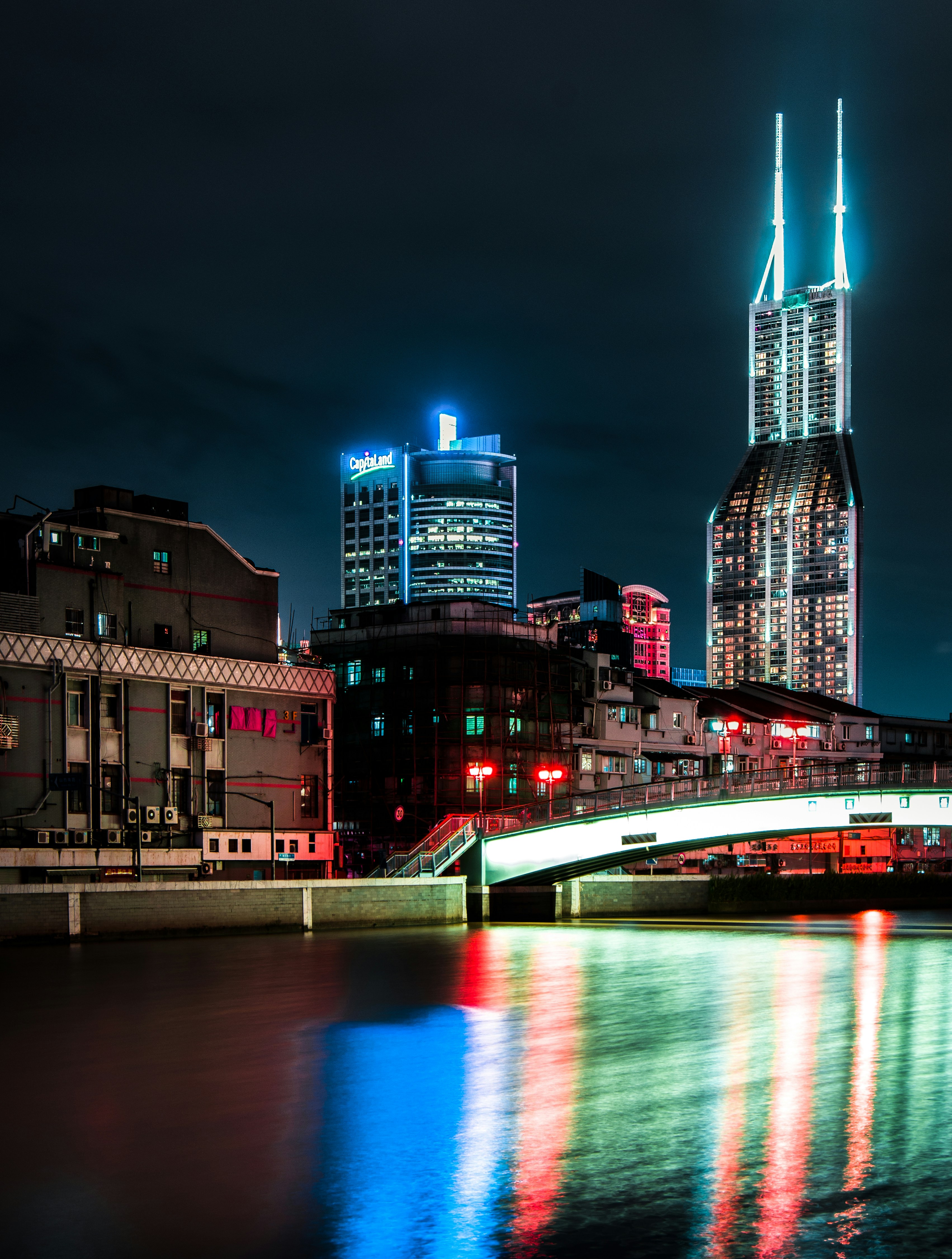 Illuminated skyline featuring modern skyscrapers and a bridge reflecting in the water at night.