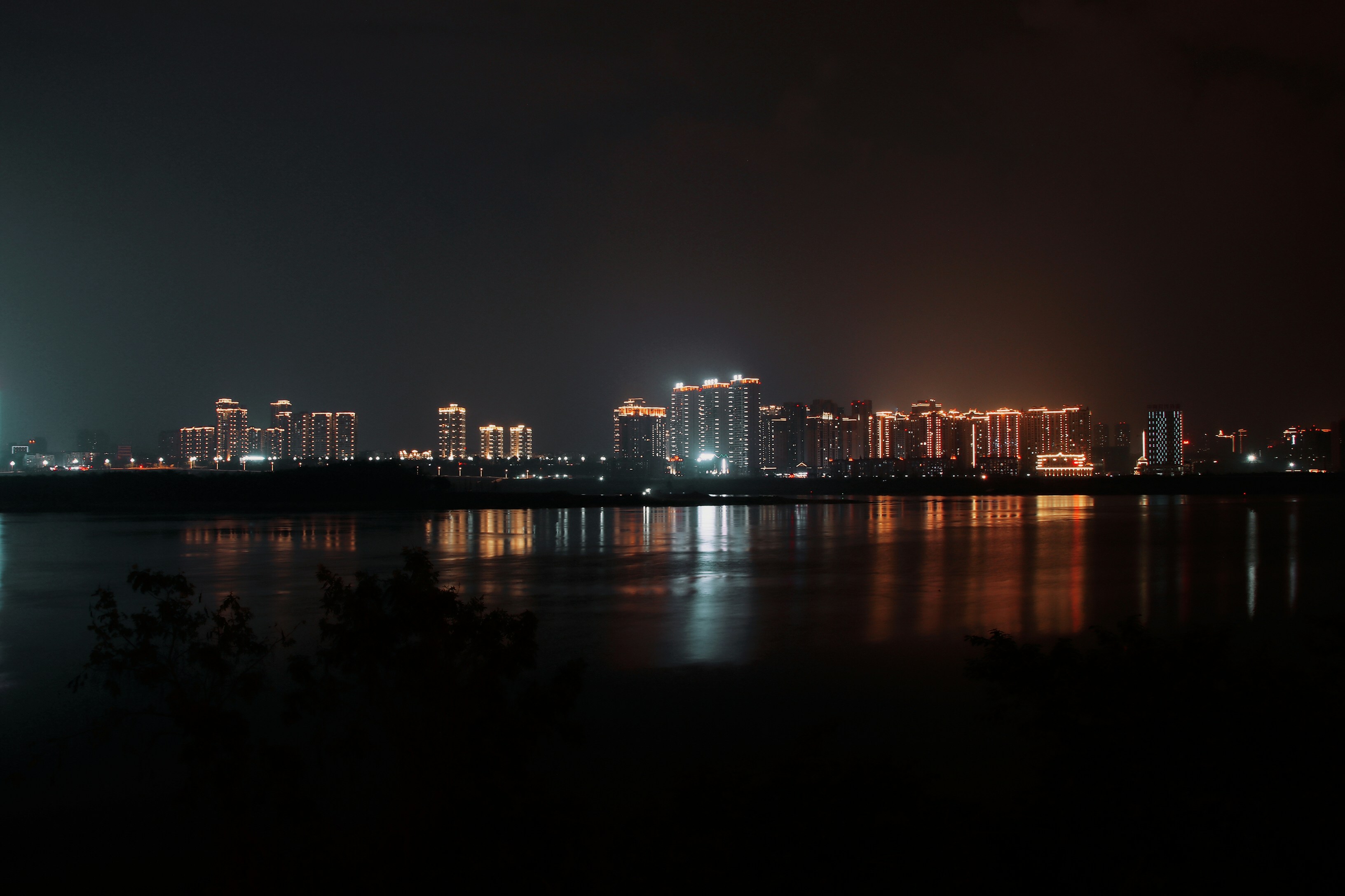 City skyline illuminated against the night sky, reflecting on a calm body of water.