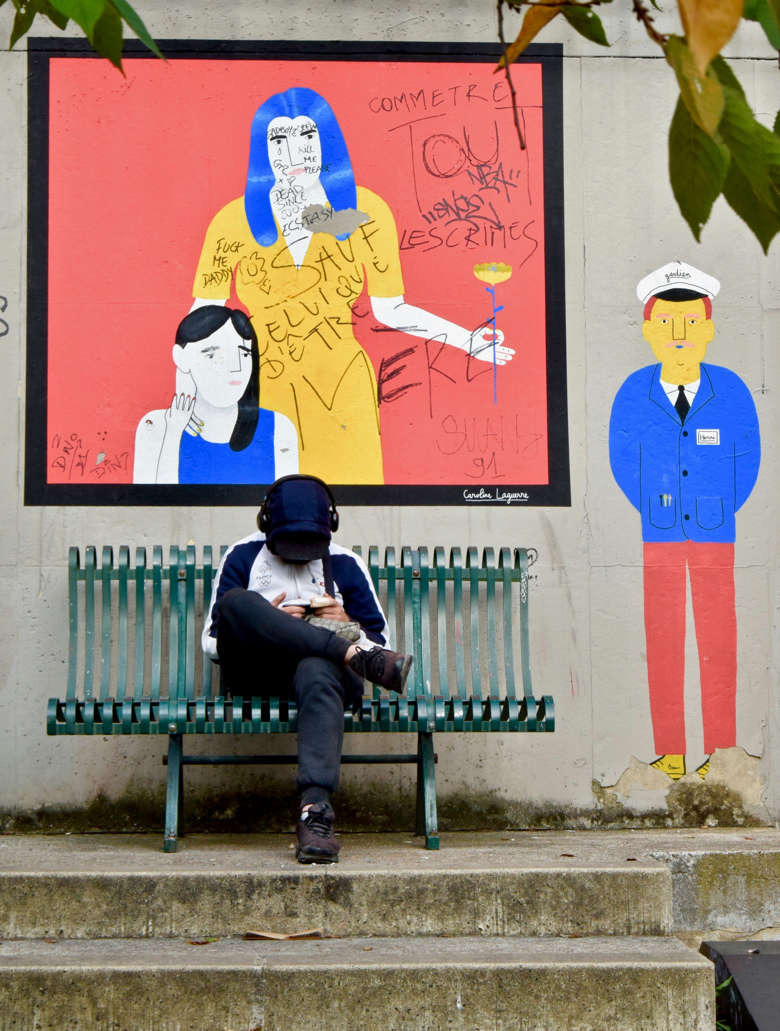 Hooded Pause Under a Wall of Colorful Portraits