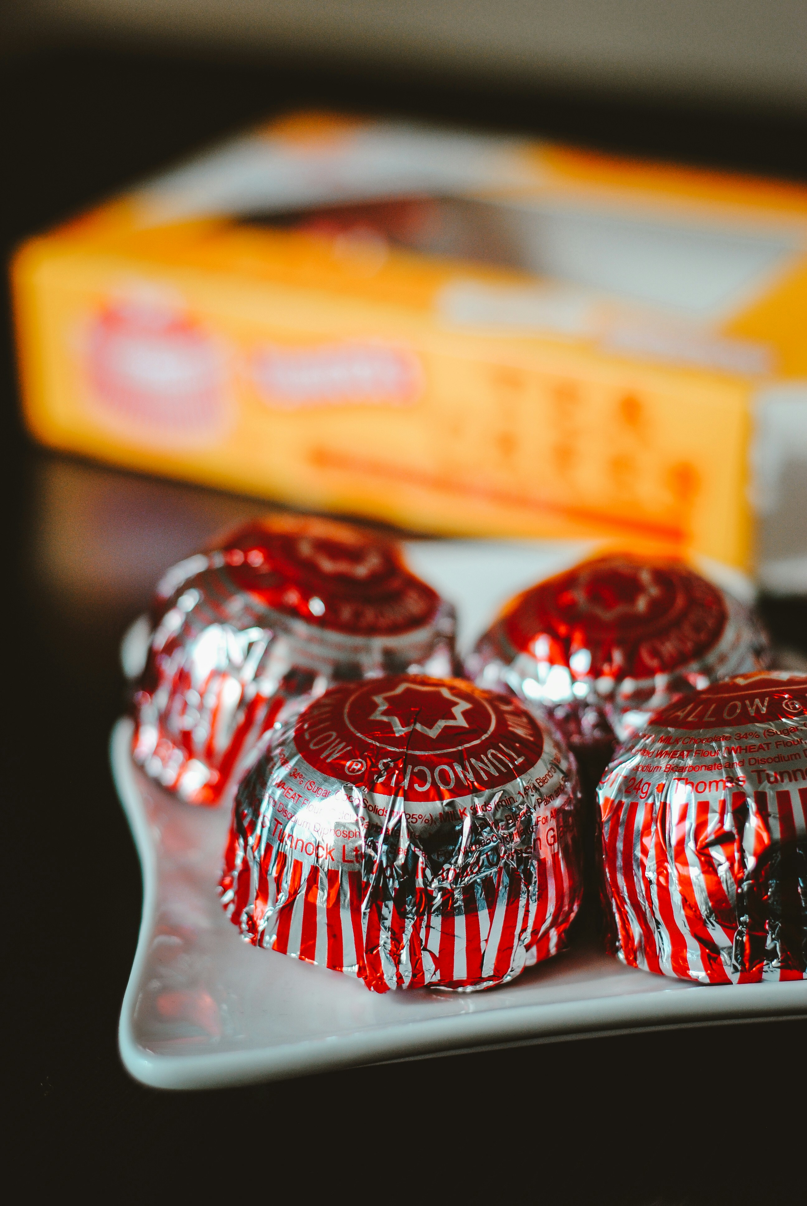 A plate of red and silver wrapped chocolates sits elegantly, with a colorful box partially visible in the background. Perfectly arranged for a tempting presentation.