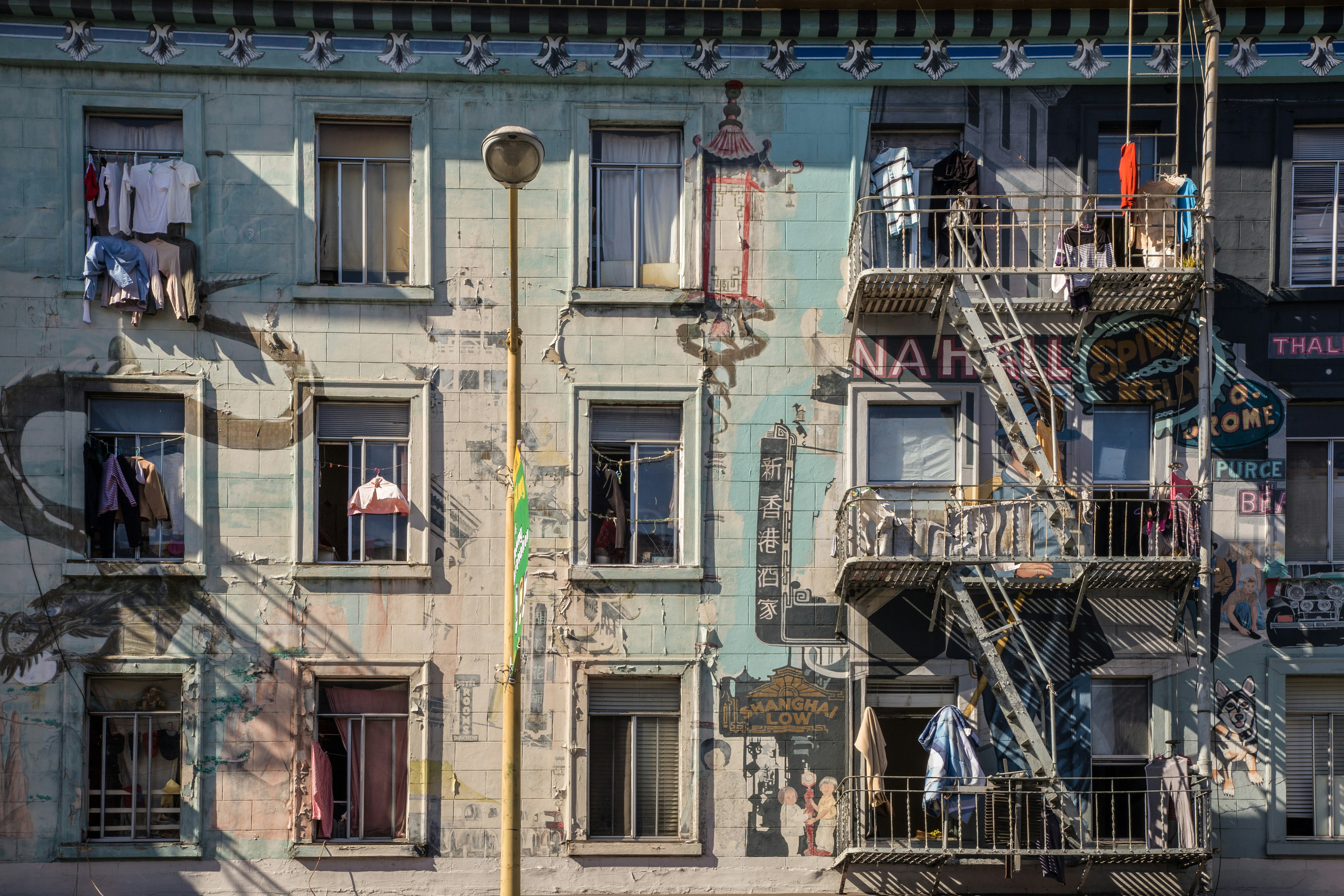 Vibrant mural-adorned building with laundry hanging from windows, showcasing urban life and culture. Fire escape adds depth to the scene.
