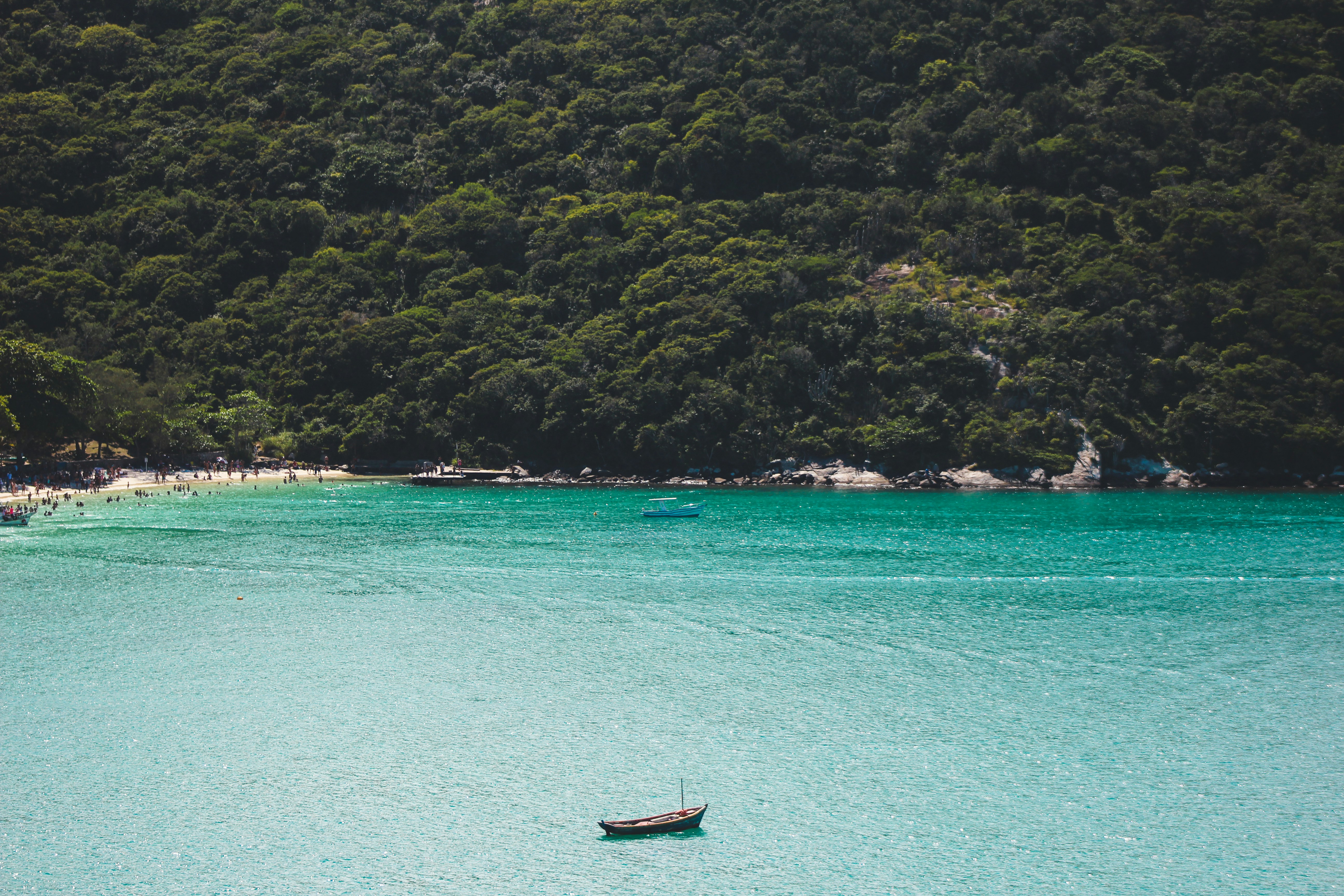 Small boat floats on clear turquoise sea near lush green coastline under a bright sky.