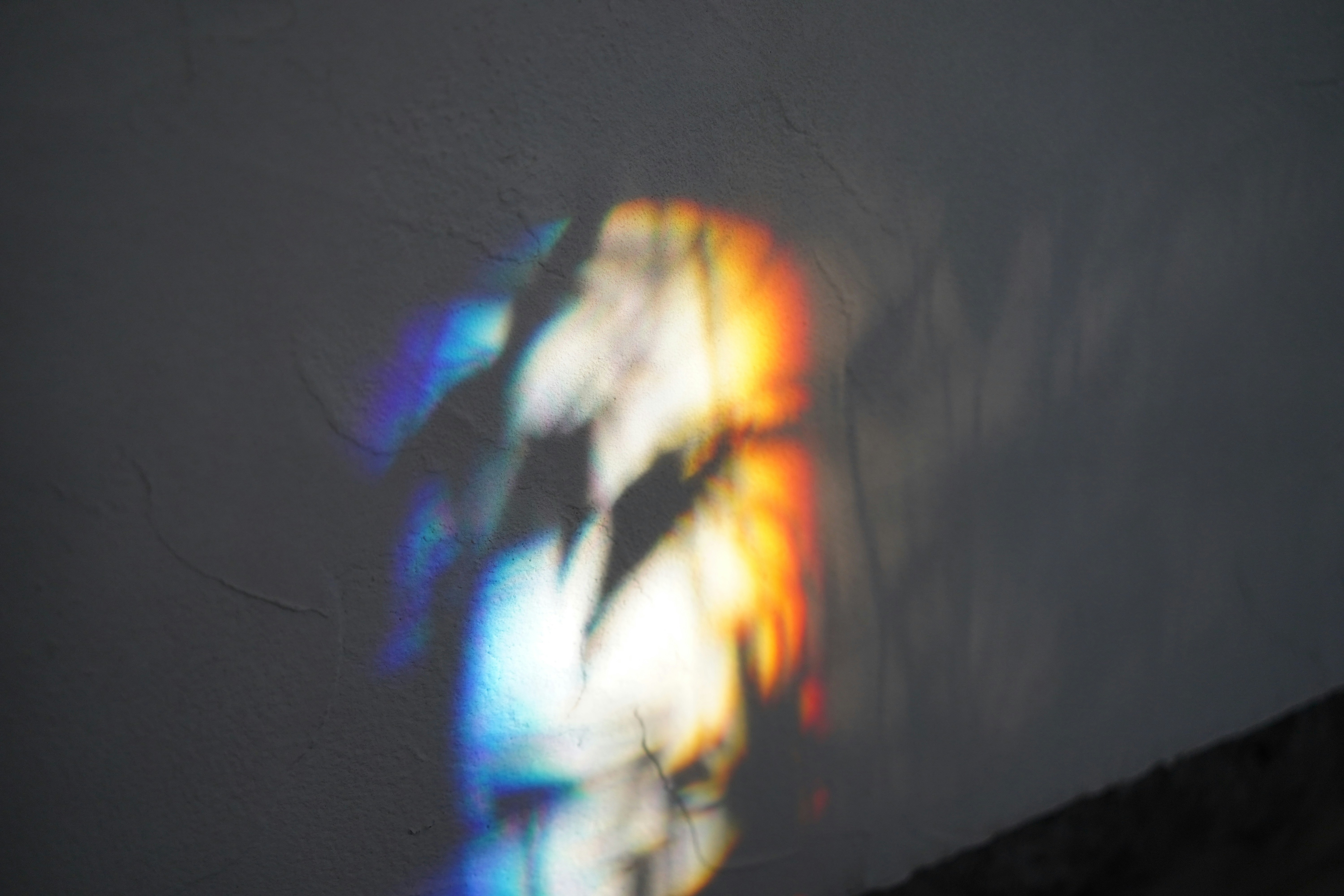 Prismatic glow on a textured wall: a fleeting rainbow over concrete