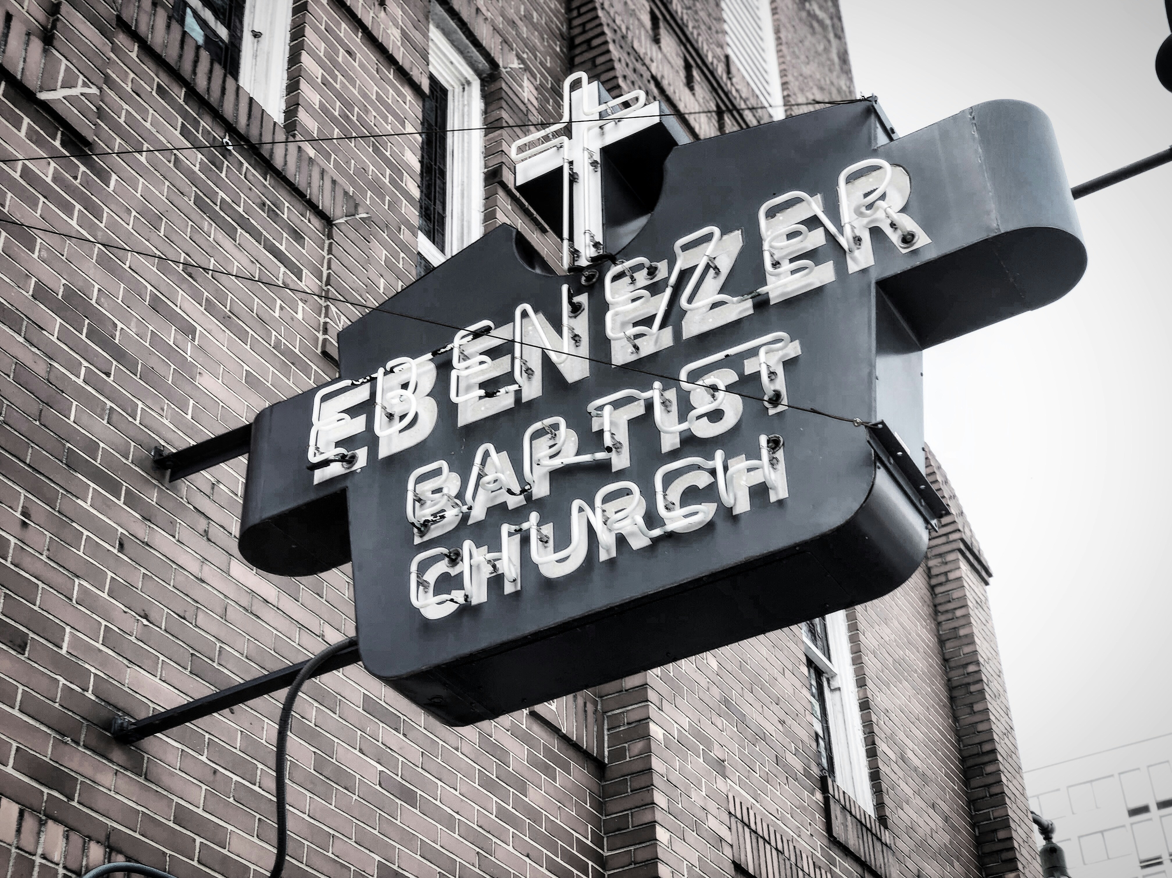 Vintage neon sign for Ebenezer Baptist Church against a brick building backdrop.