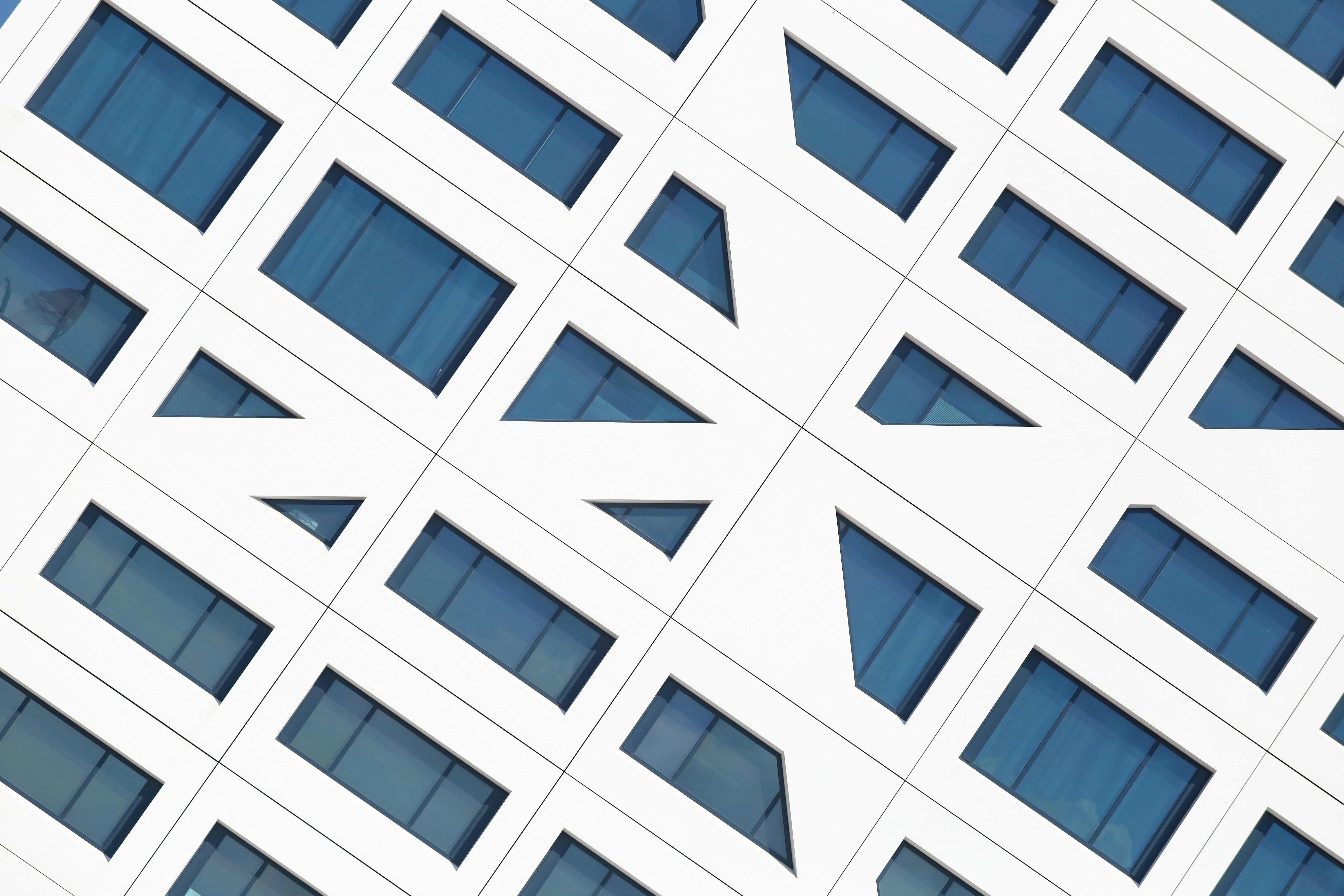 Abstract view of a building's facade featuring geometric patterns and reflective windows. The design emphasizes symmetry and contemporary architecture.