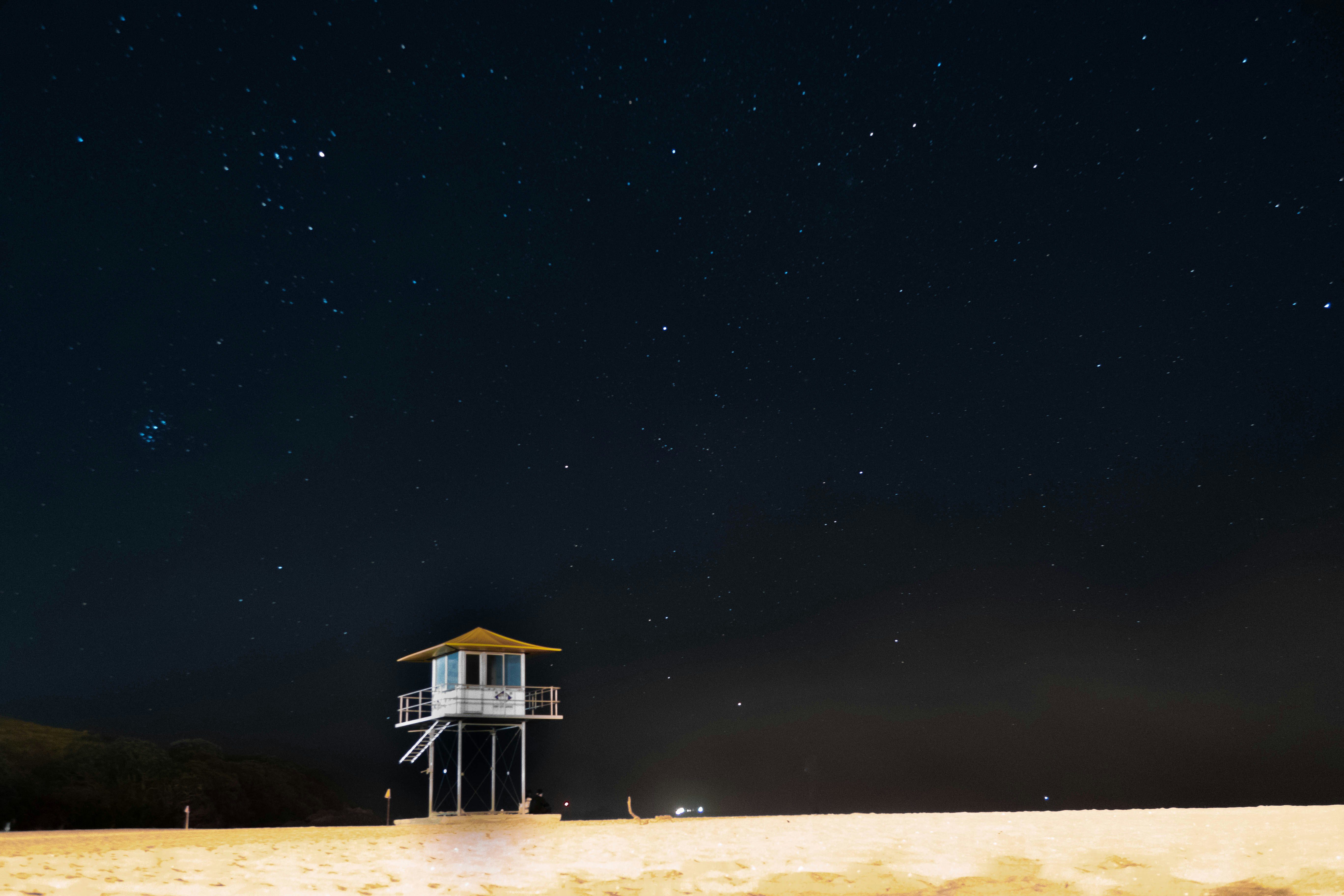 Lifeguard tower stands alone on a sandy beach beneath a star-filled night sky.