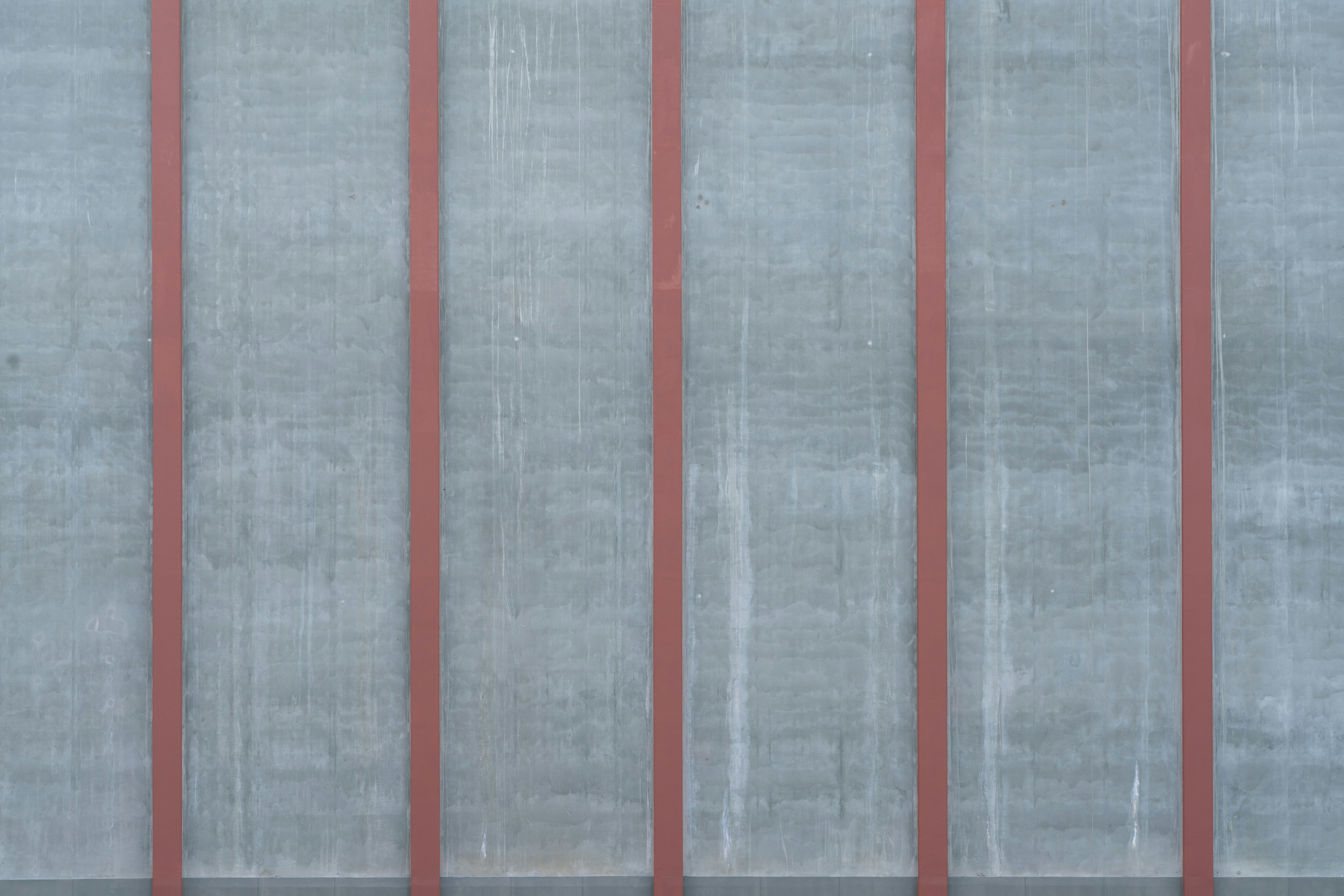 Textured concrete wall segmented by bold red vertical beams, showcasing industrial design elements.