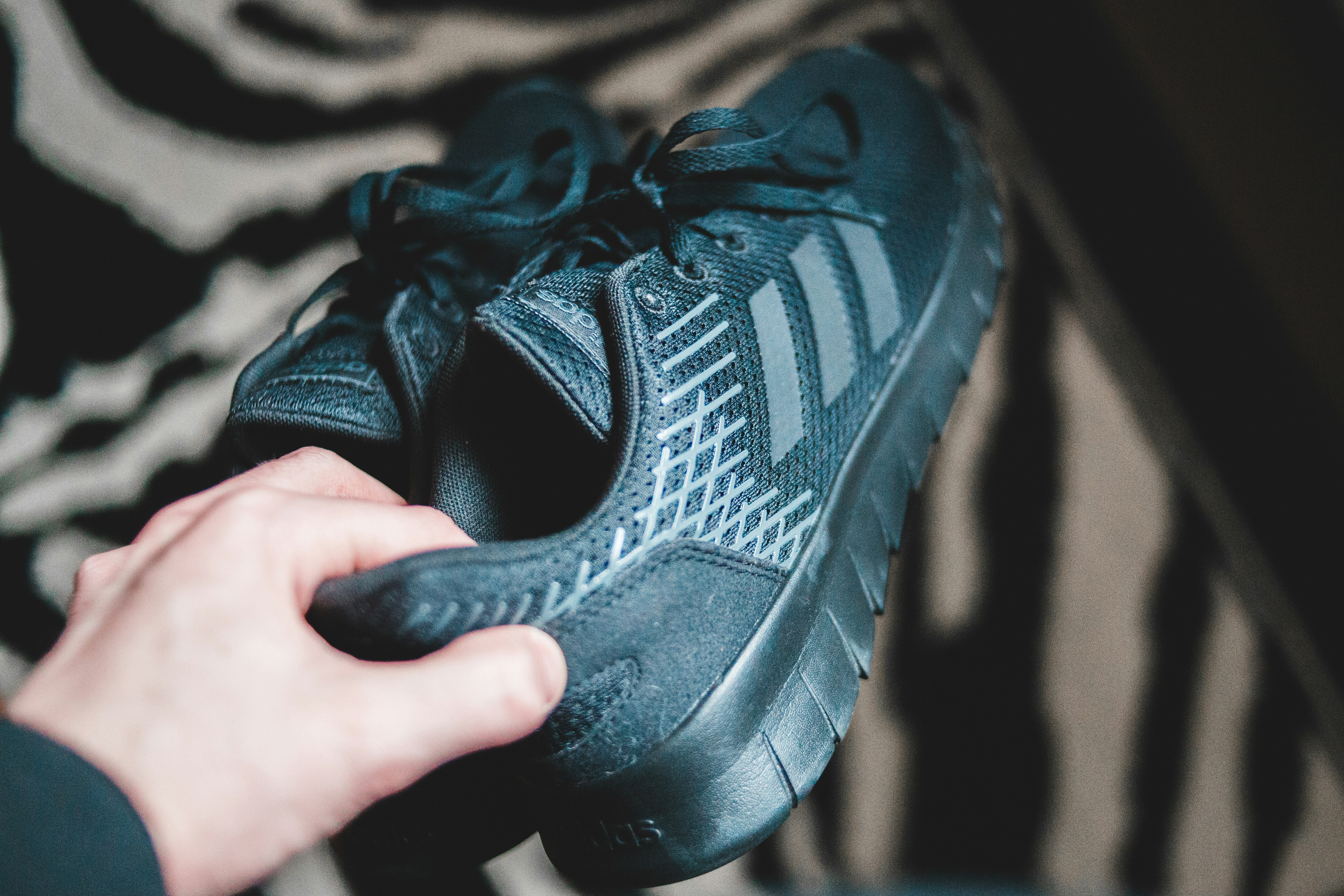 Black Adidas running shoes held above black and white carper photo ...