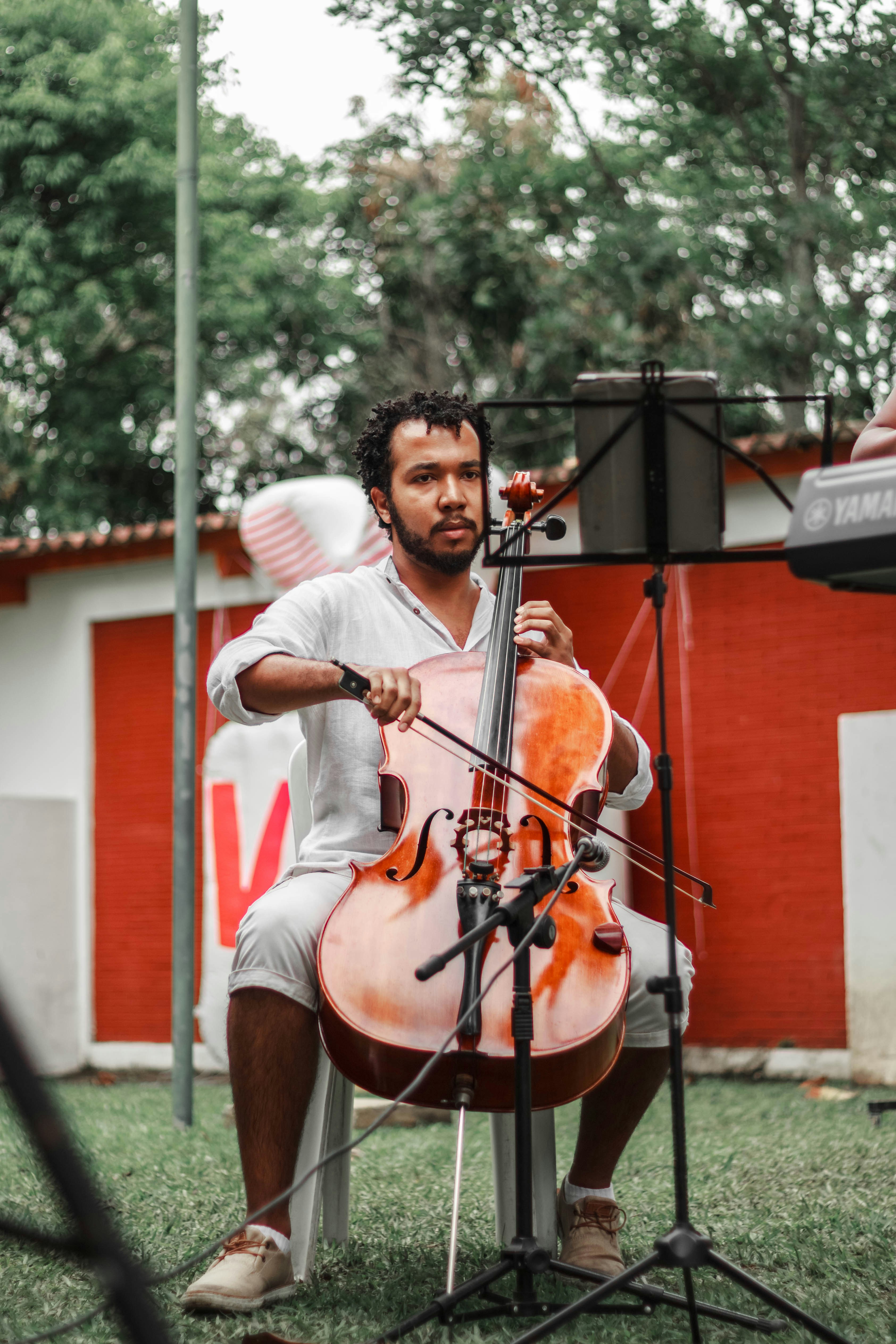 Musician passionately playing the cello in a vibrant outdoor setting, surrounded by greenery and colorful decor.